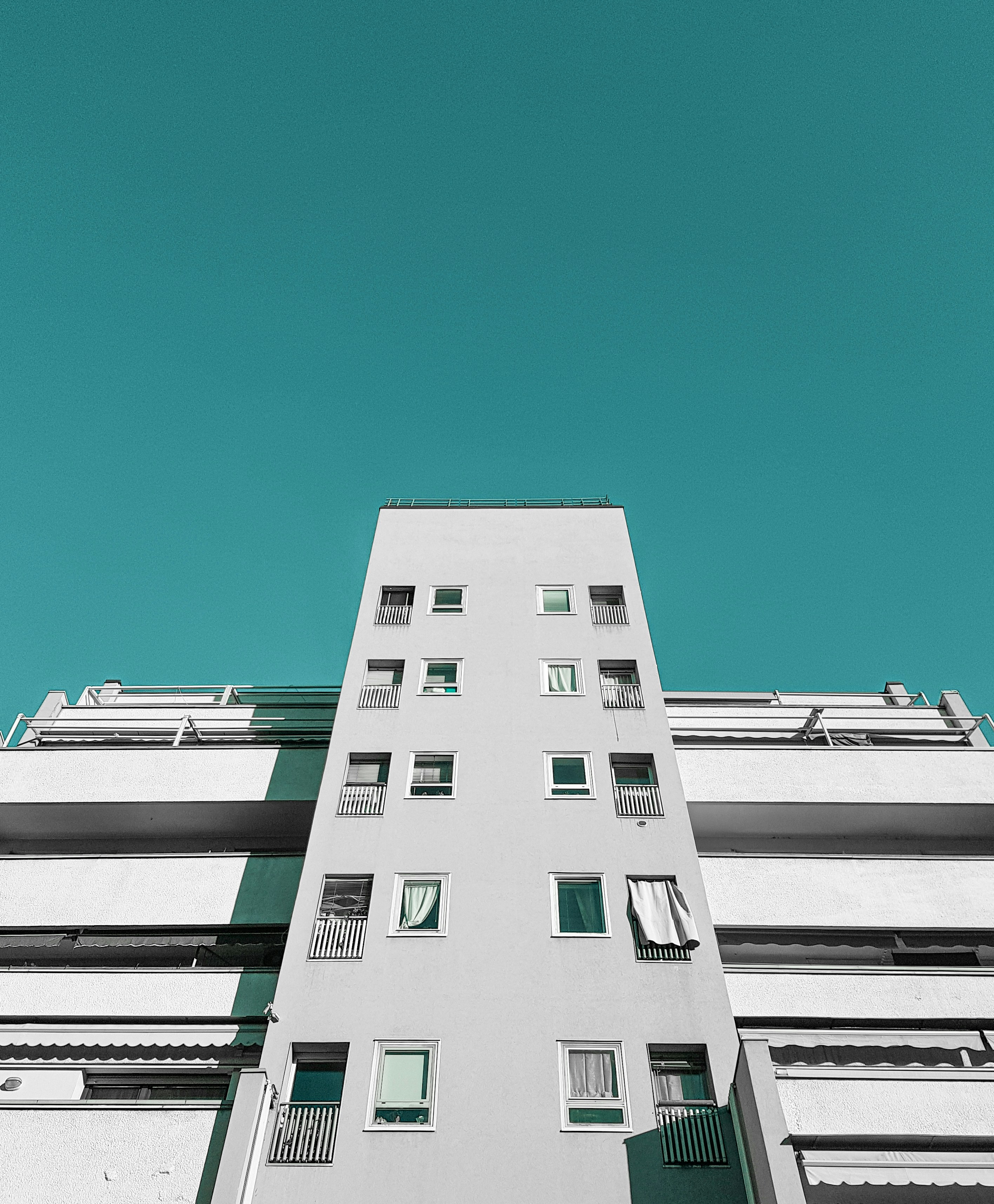 White apartment tower rises against a minimalist urban facade beneath a vivid teal sky.