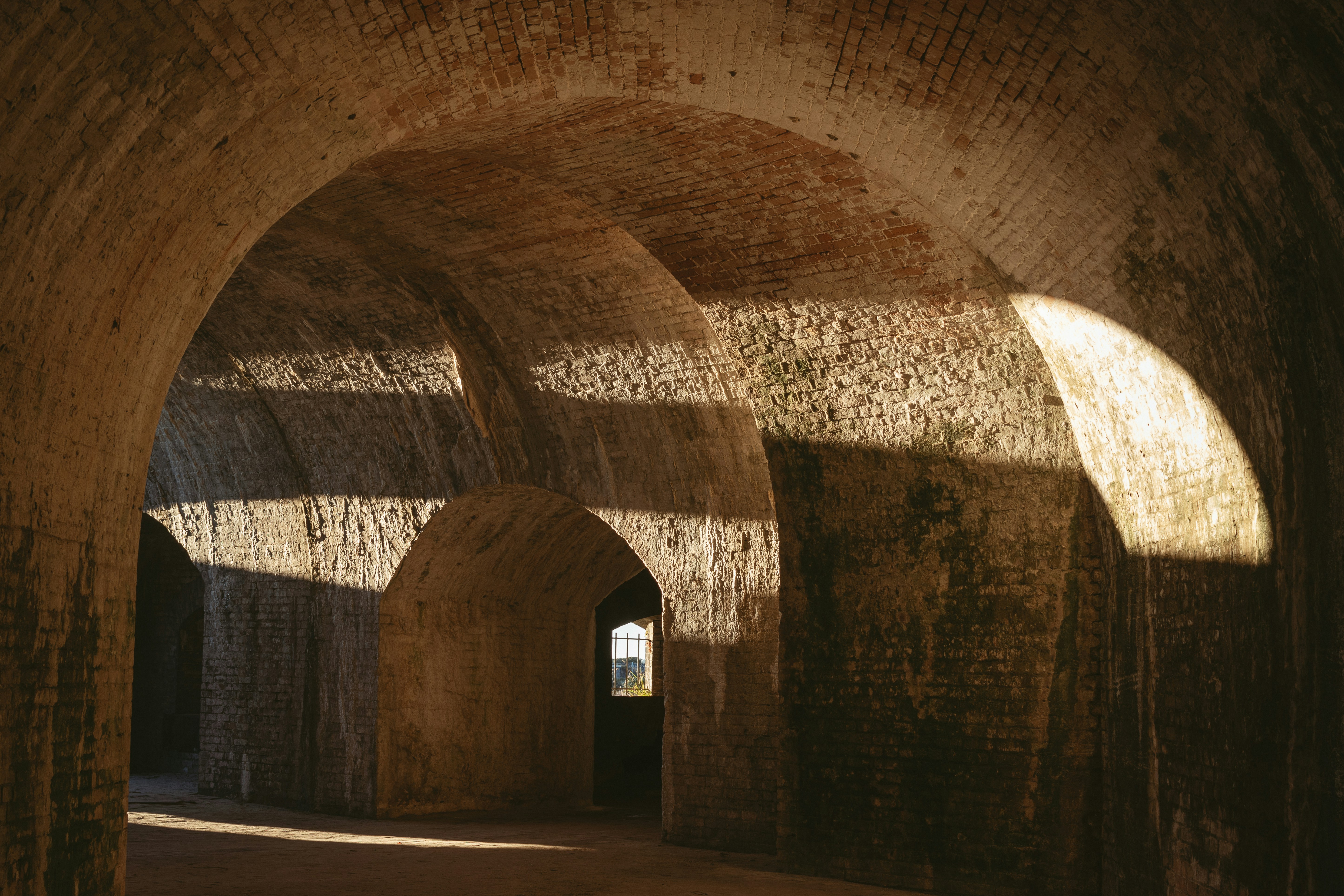 Sunlight streams through arched stone corridors, casting geometric shadows on textured walls.