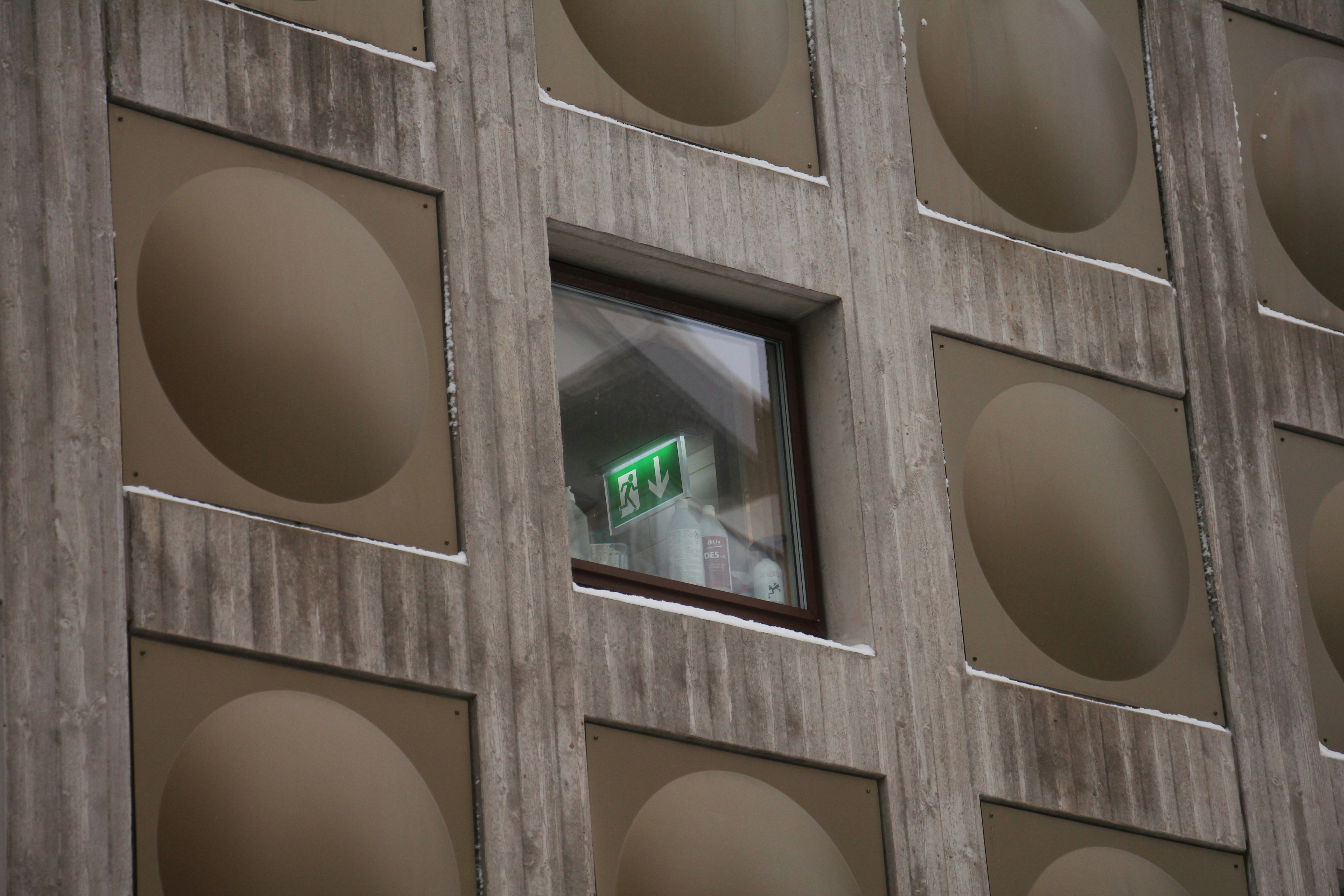 Window framed by unique architectural elements, featuring a visible exit sign. The contrast between the smooth facade and the functional interior is striking.