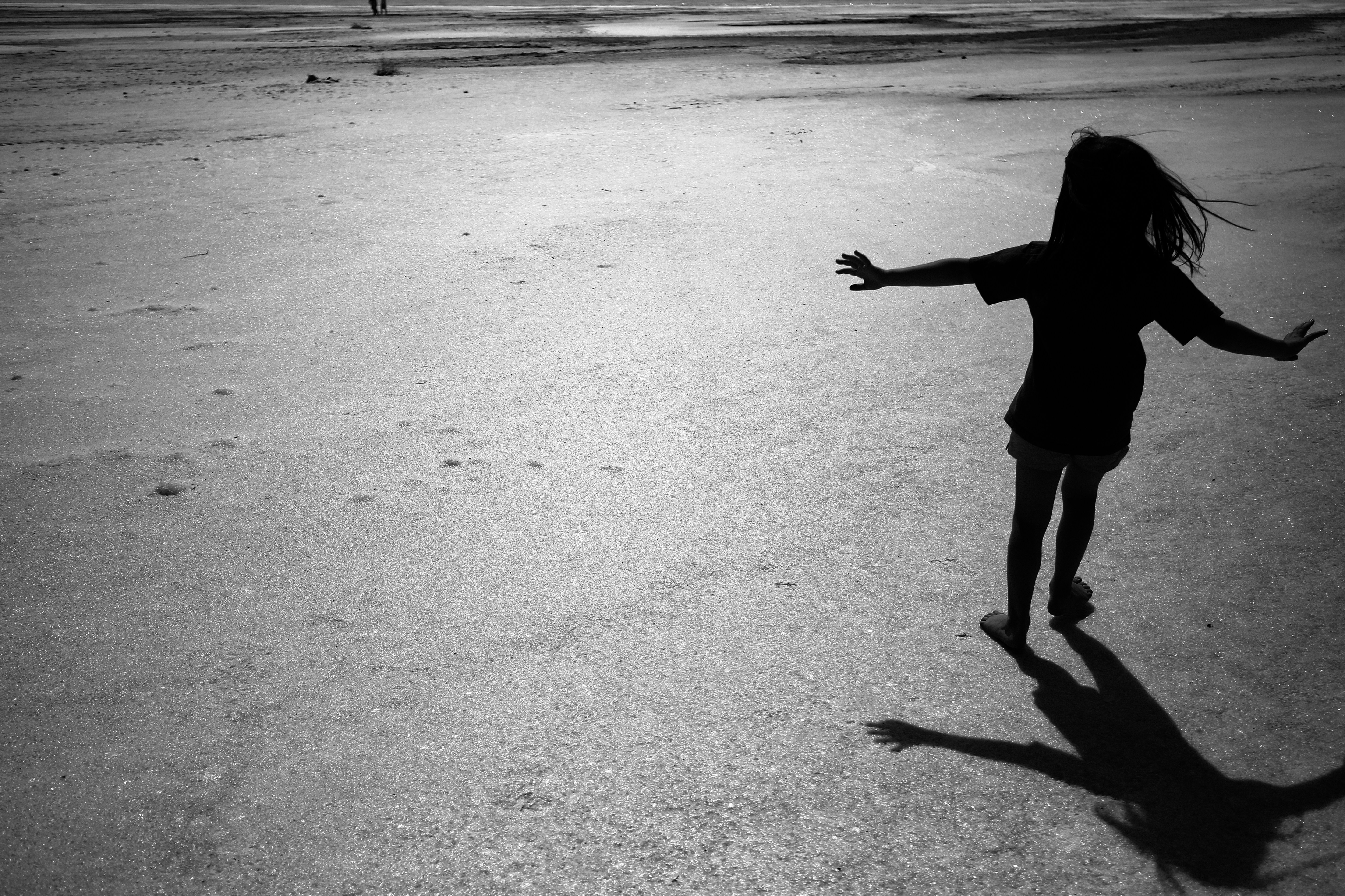 Silhouette of a child running across a sunlit pavement, casting a long shadow.