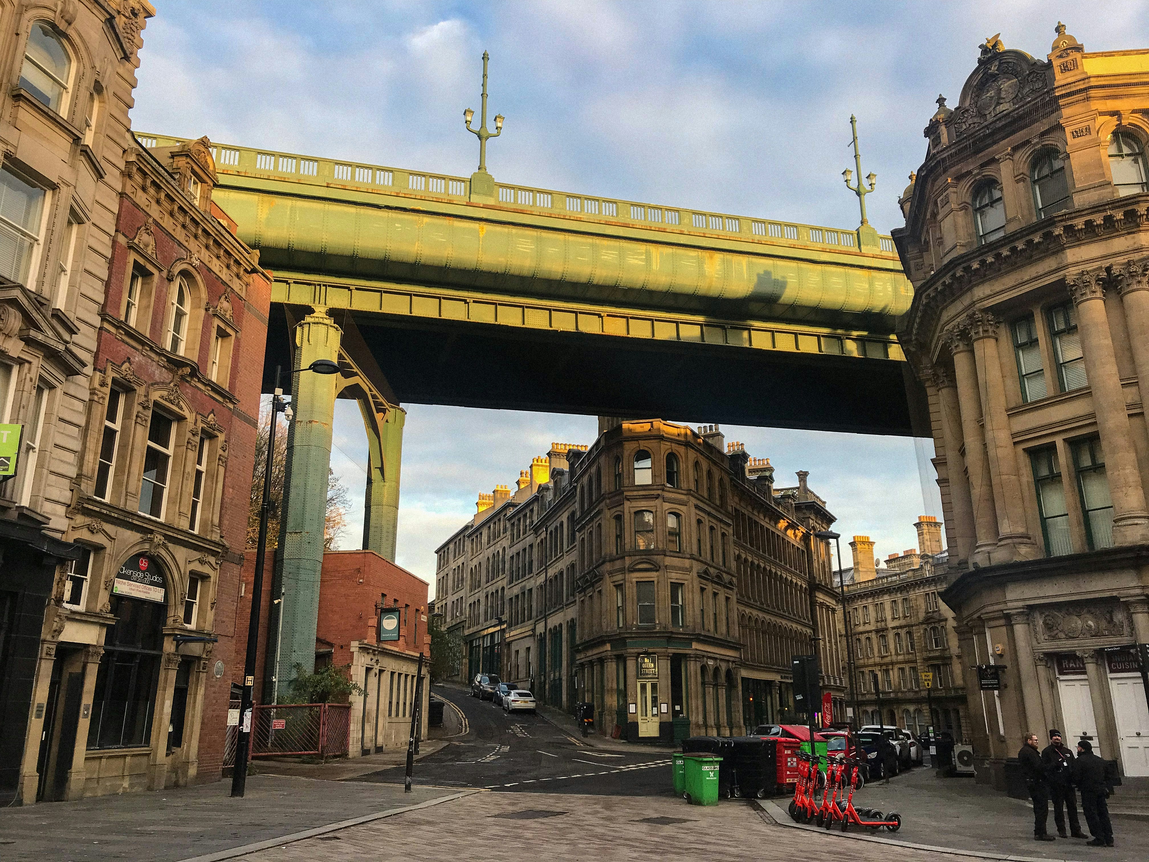 Elevated bridge spanning across a city street lined with historic buildings under a blue sky.