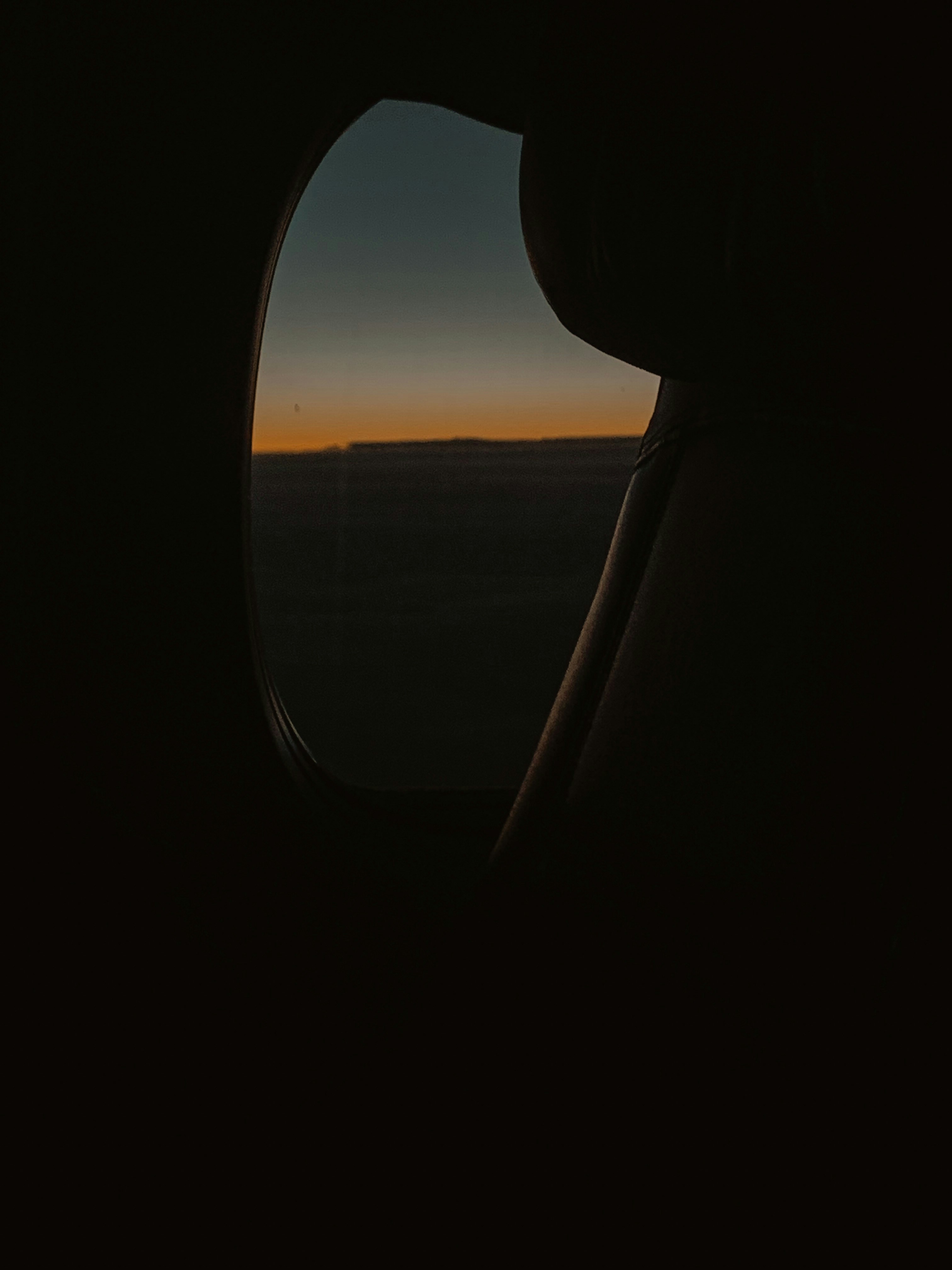 Sunset view from an airplane window, showcasing a gradient of colors against a backdrop of clouds. The silhouette of the seat adds a sense of intimacy to the scene.