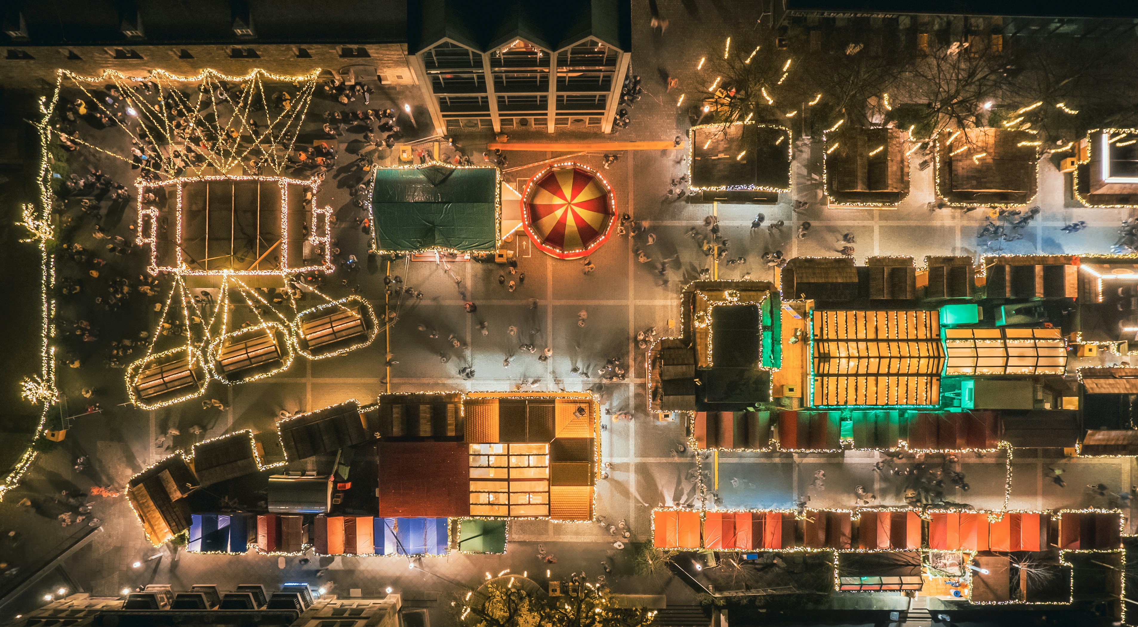 Overhead view of a brightly lit carnival at night with vivid geometric patterns.