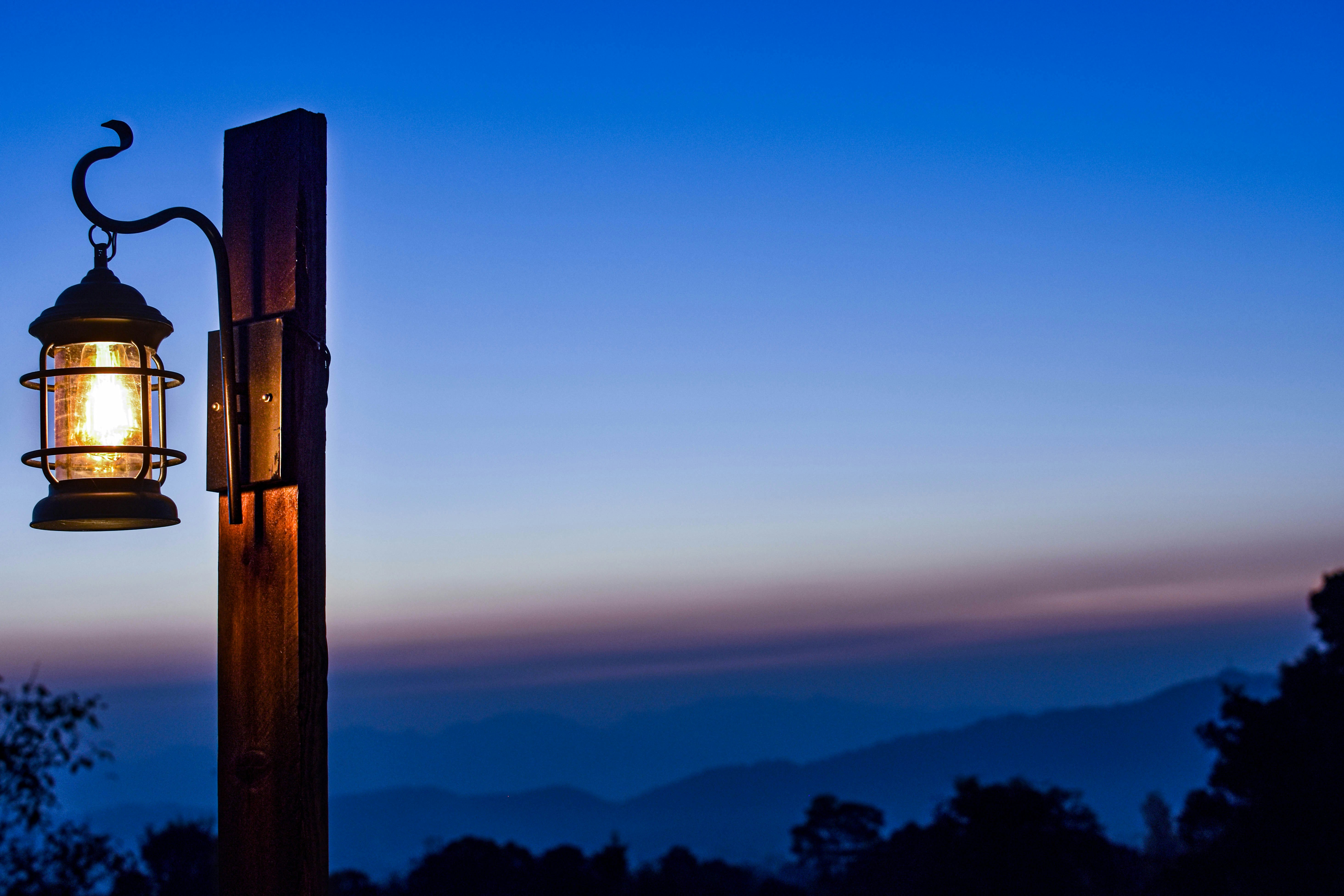 Vintage lantern casting a warm glow atop a wooden post against a twilight backdrop of rolling mountains. 