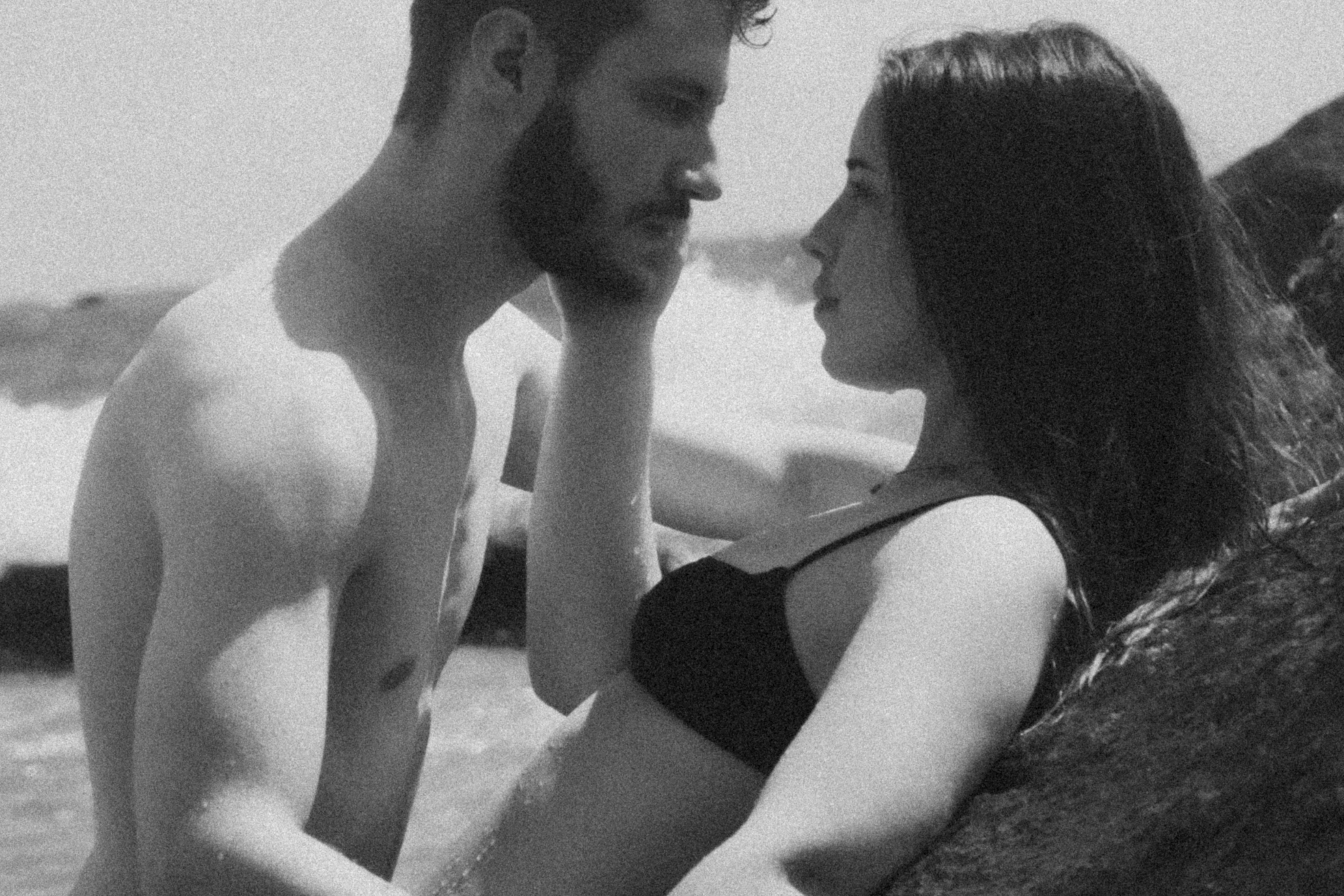 Couple sharing an intimate moment on a rocky beach, with waves crashing in the background.