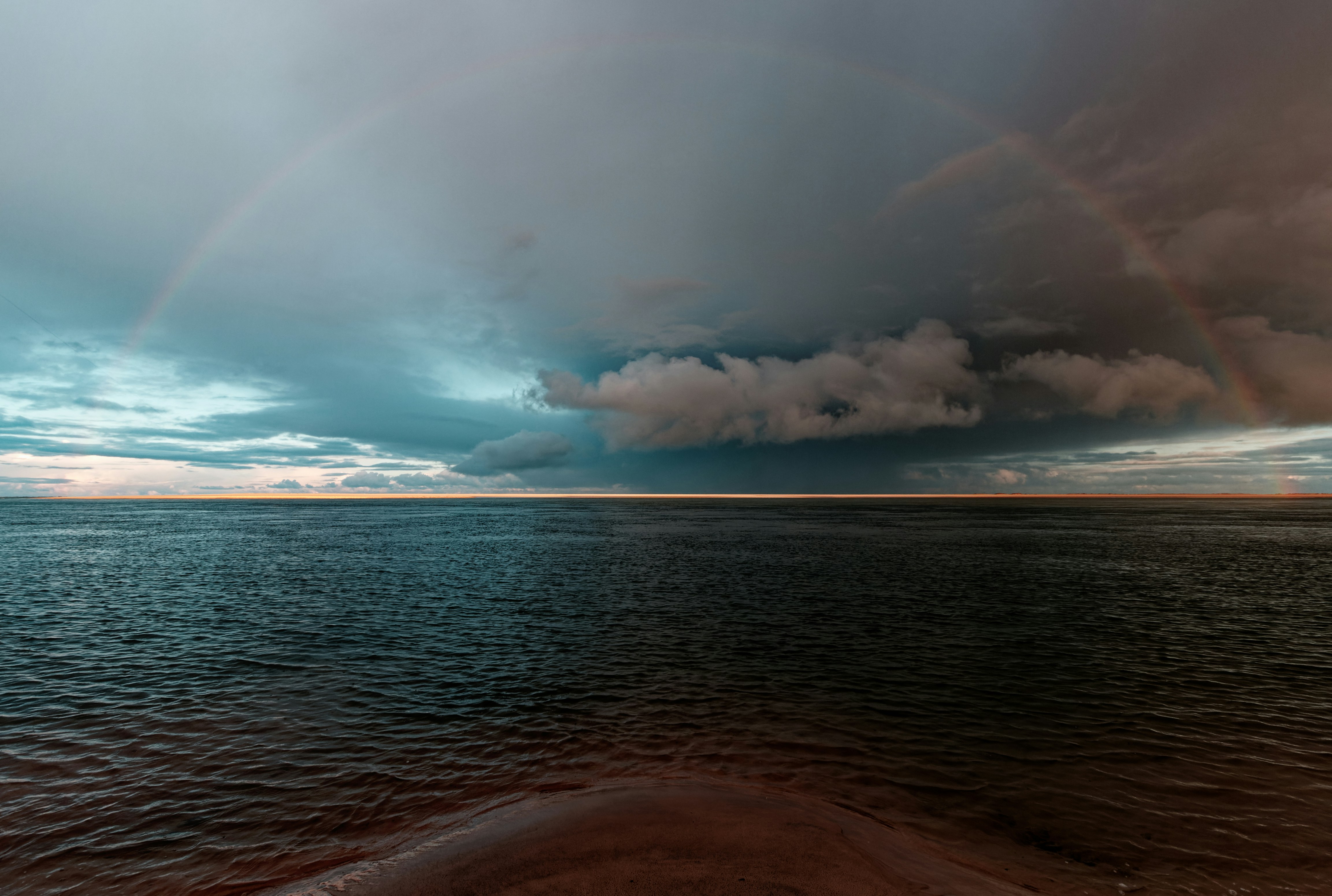 Ocean view with a distant storm cloud and a faint rainbow arching across the sky.