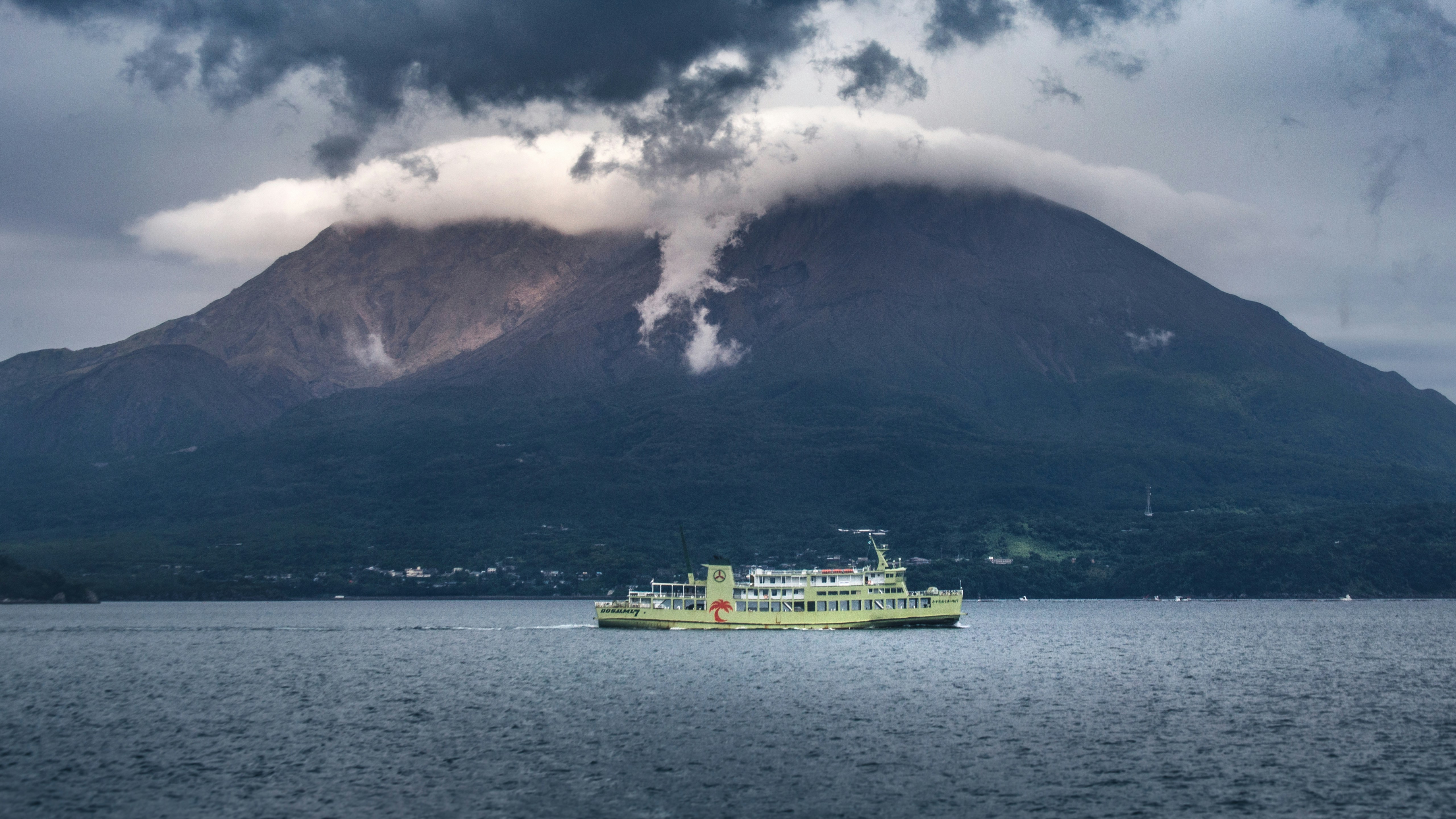 Yellow Ferry Crossing a Tranquil Lake Beneath a Cloud-Wrapped Volcano