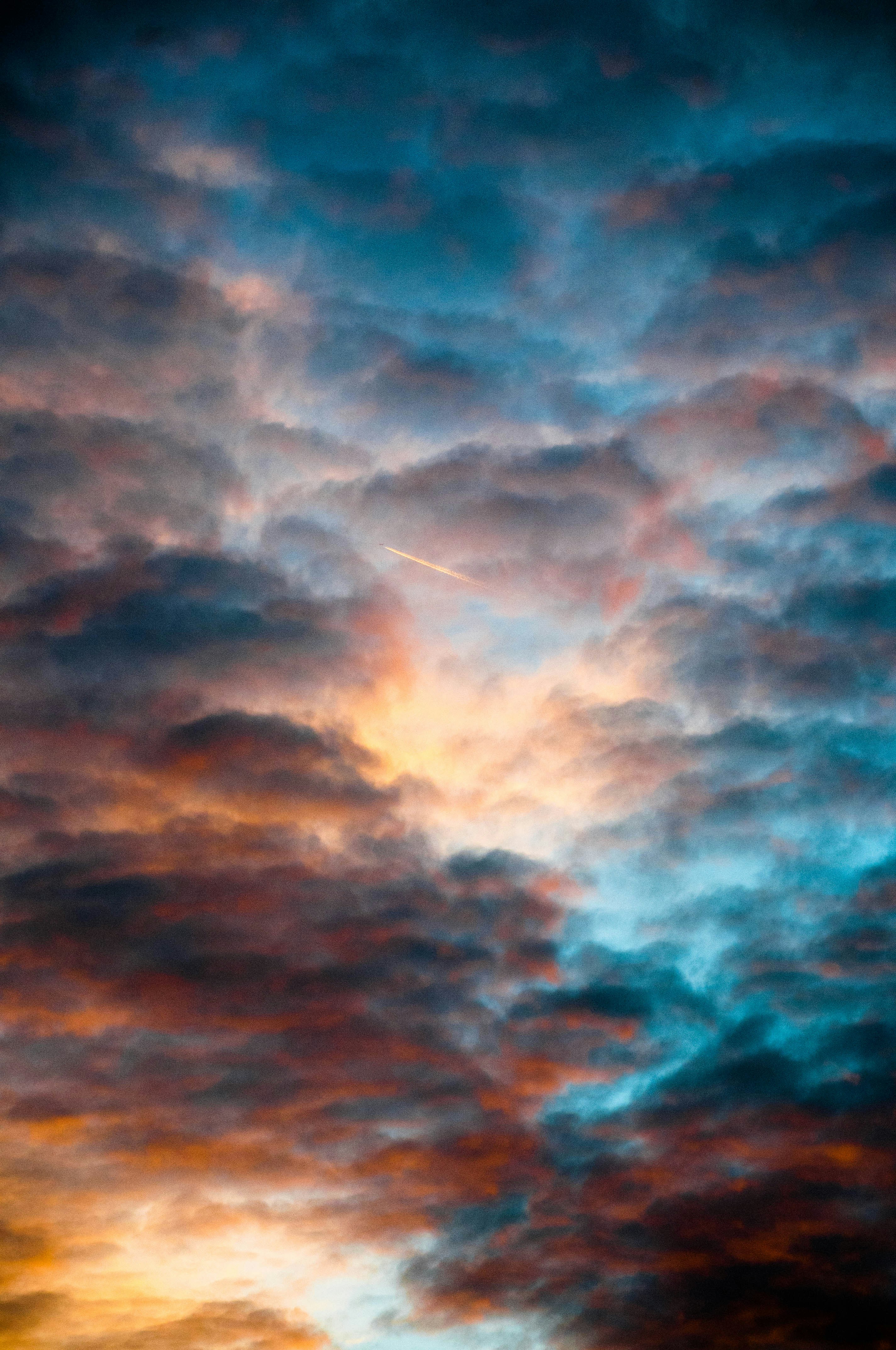 Vibrant sunset clouds painted in shades of blue, orange, and pink, with a faint trail of an aircraft visible. The scene evokes a sense of tranquility and wonder.