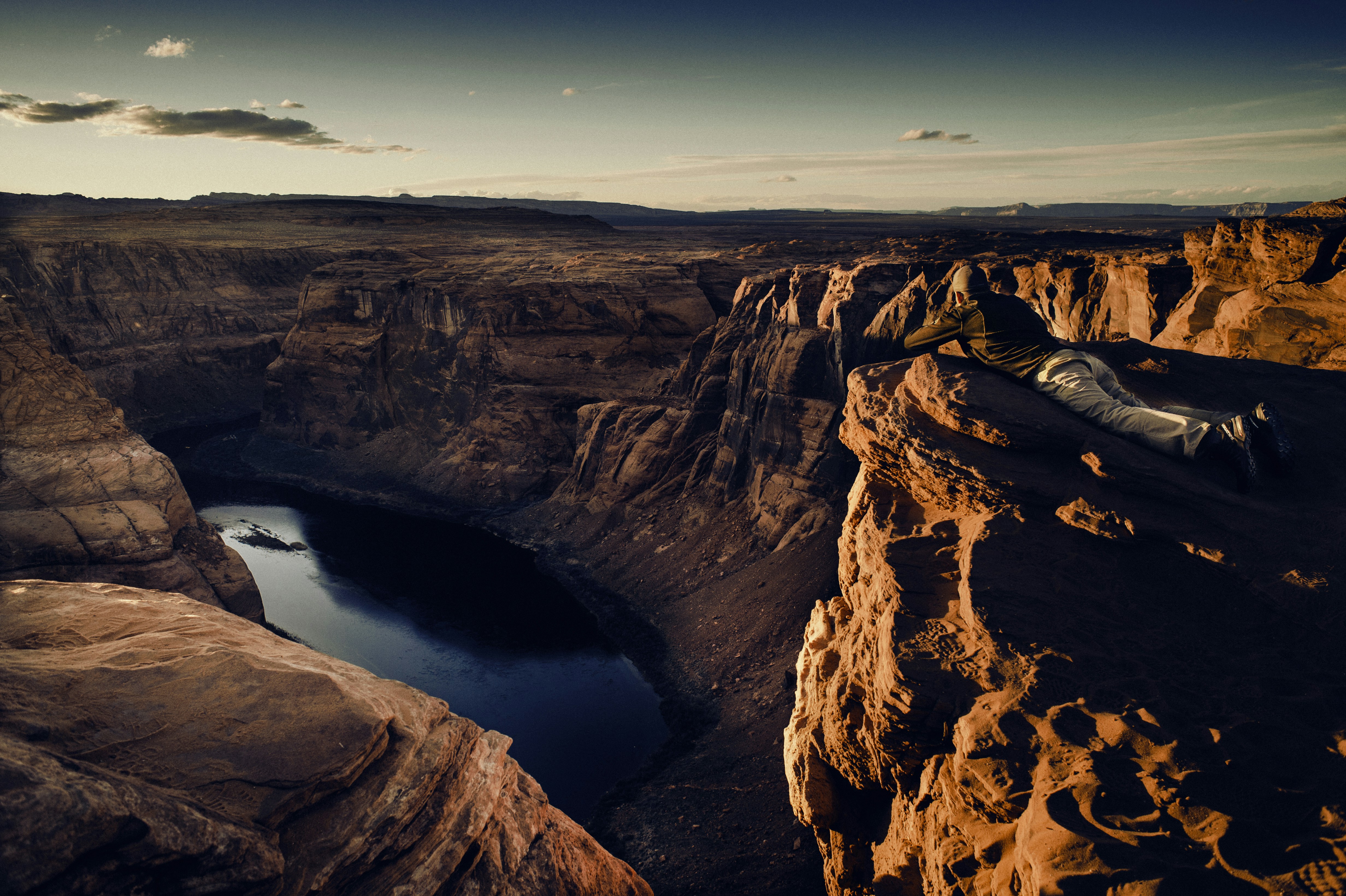 A man laying on top of a cliff next to a lake photo – Free Canyon Image ...
