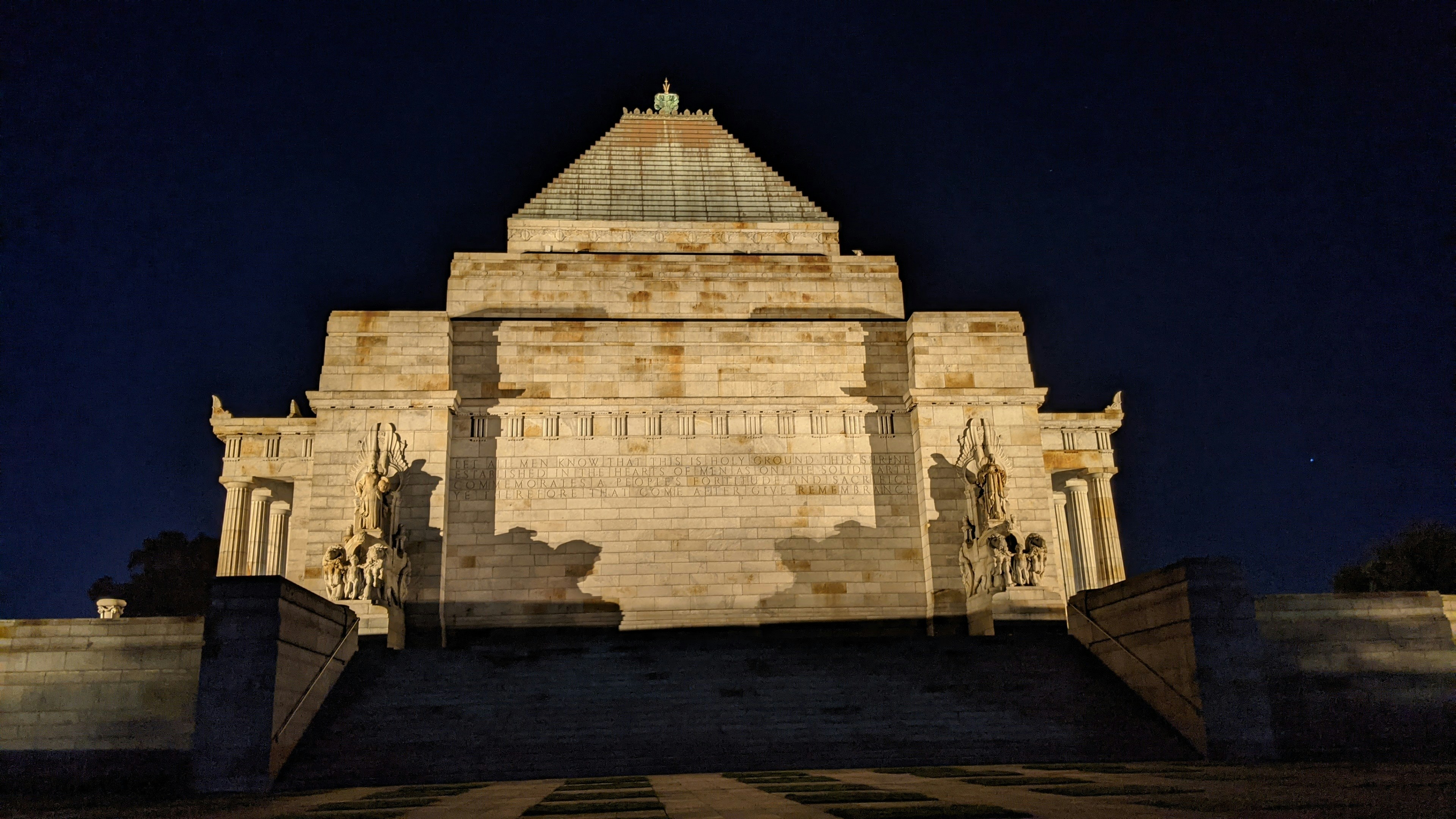 Illuminated war memorial at night, showcasing intricate architectural details and dramatic shadows.