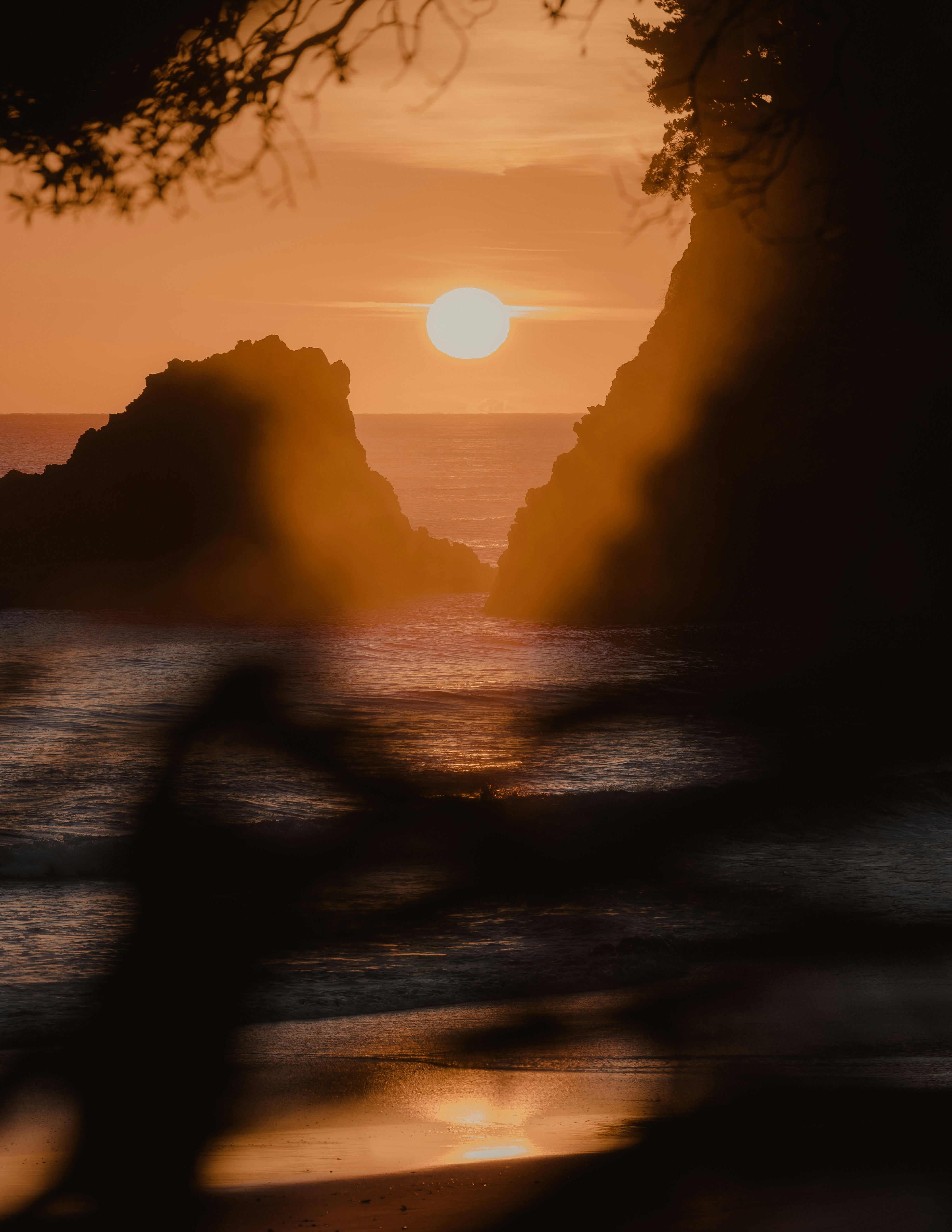 Sunset casting warm light between rocky sea stacks on a beach.