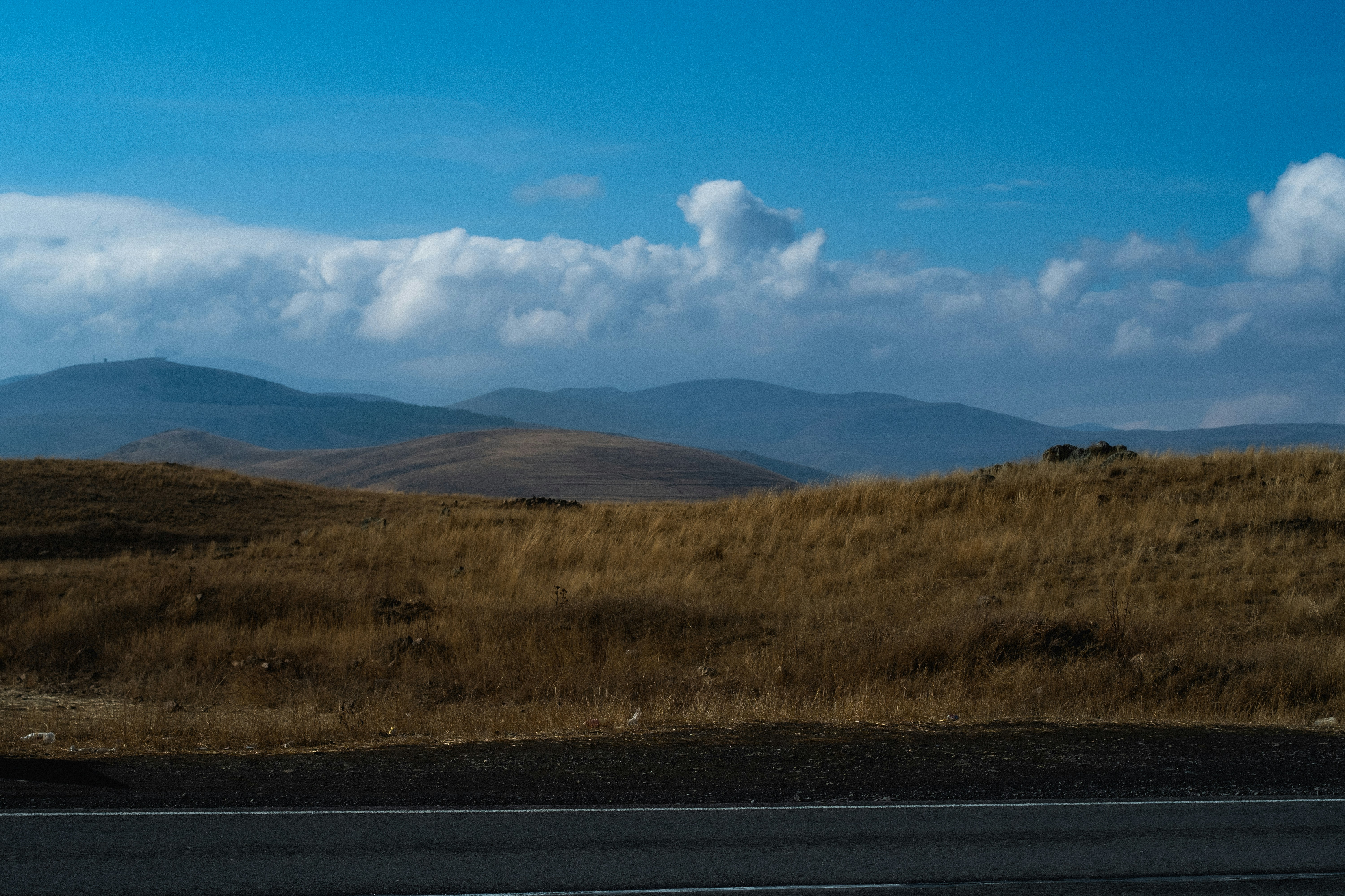 Golden grasslands stretch beneath a vast sky, with distant mountains softly fading into the horizon.