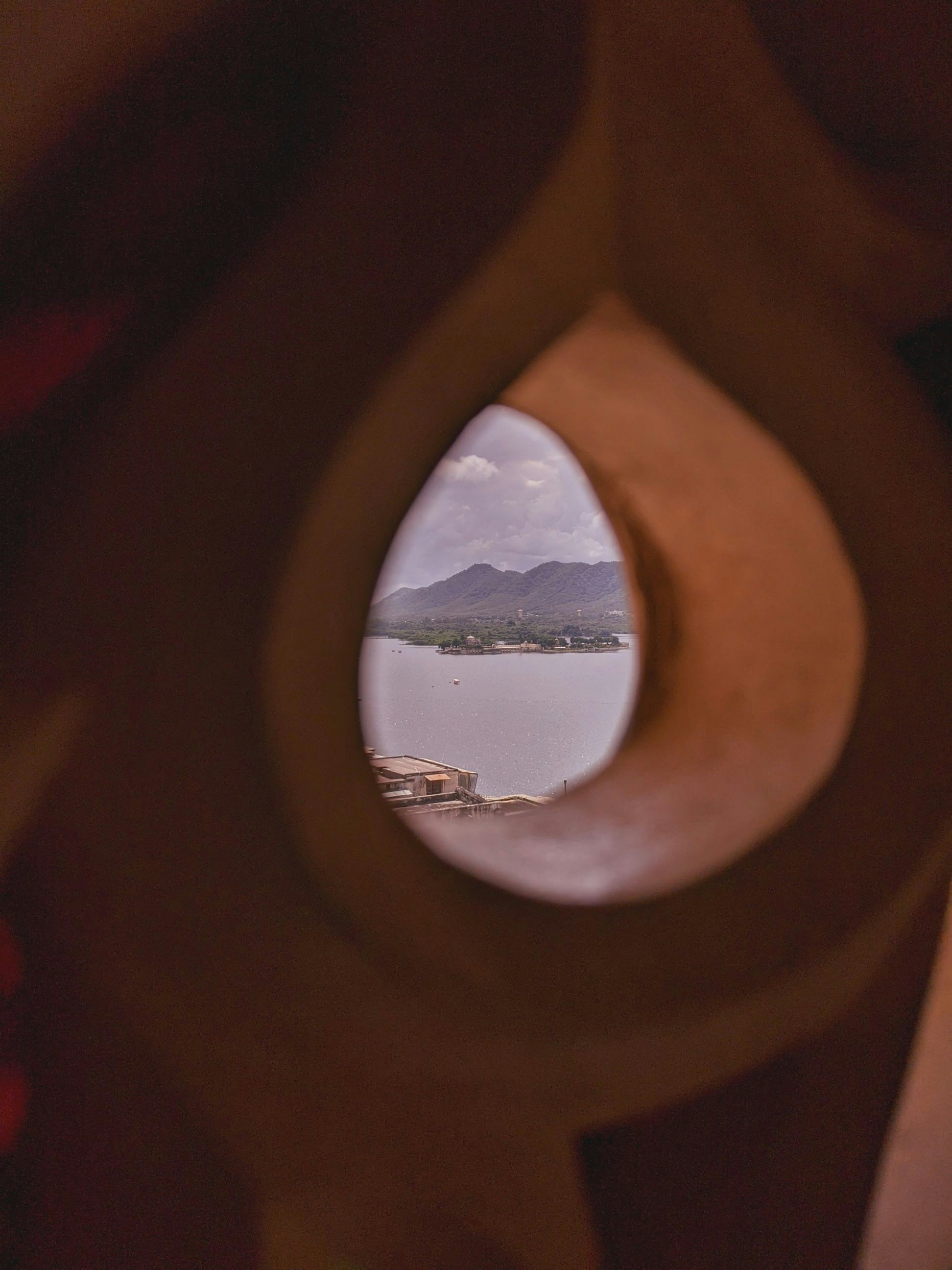 View of a tranquil lake and distant mountains through a decorative opening. The scene captures the harmony between architecture and nature.