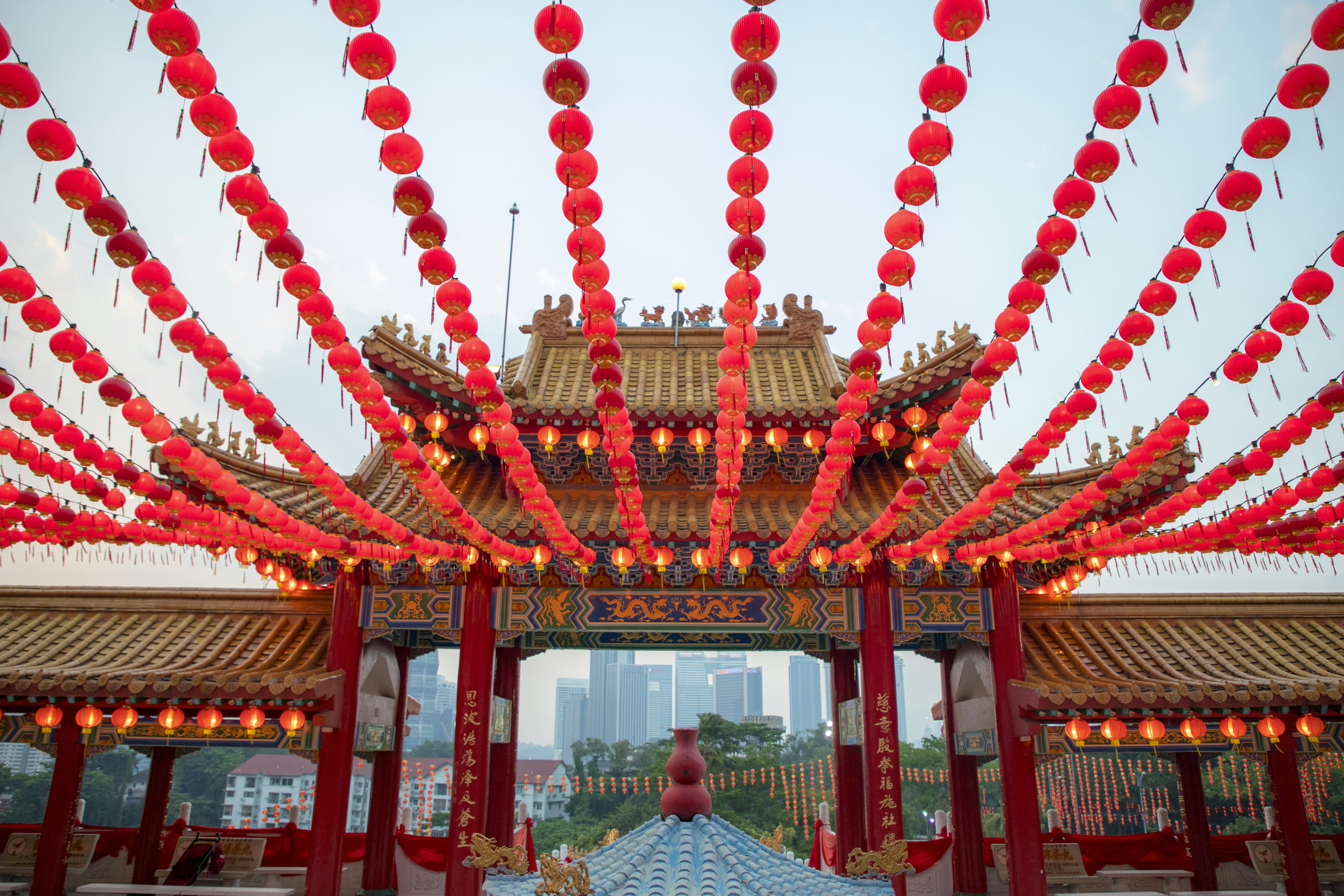 Vibrant red lanterns adorn a traditional temple, creating a festive atmosphere against a backdrop of modern skyscrapers. The intricate architectural details reflect cultural heritage.
