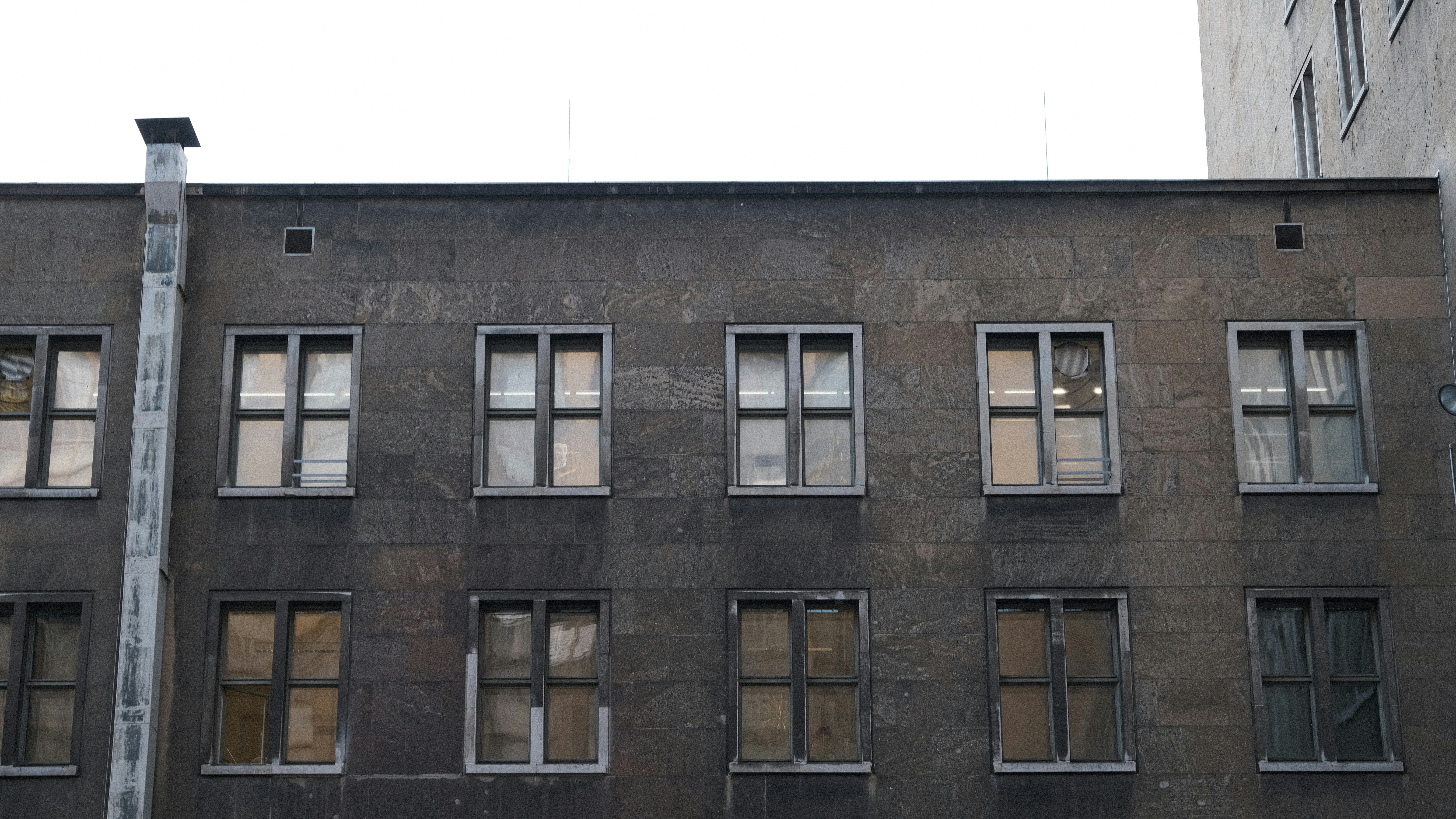 A close-up view of a textured building facade featuring a series of windows, showcasing architectural symmetry and muted tones.