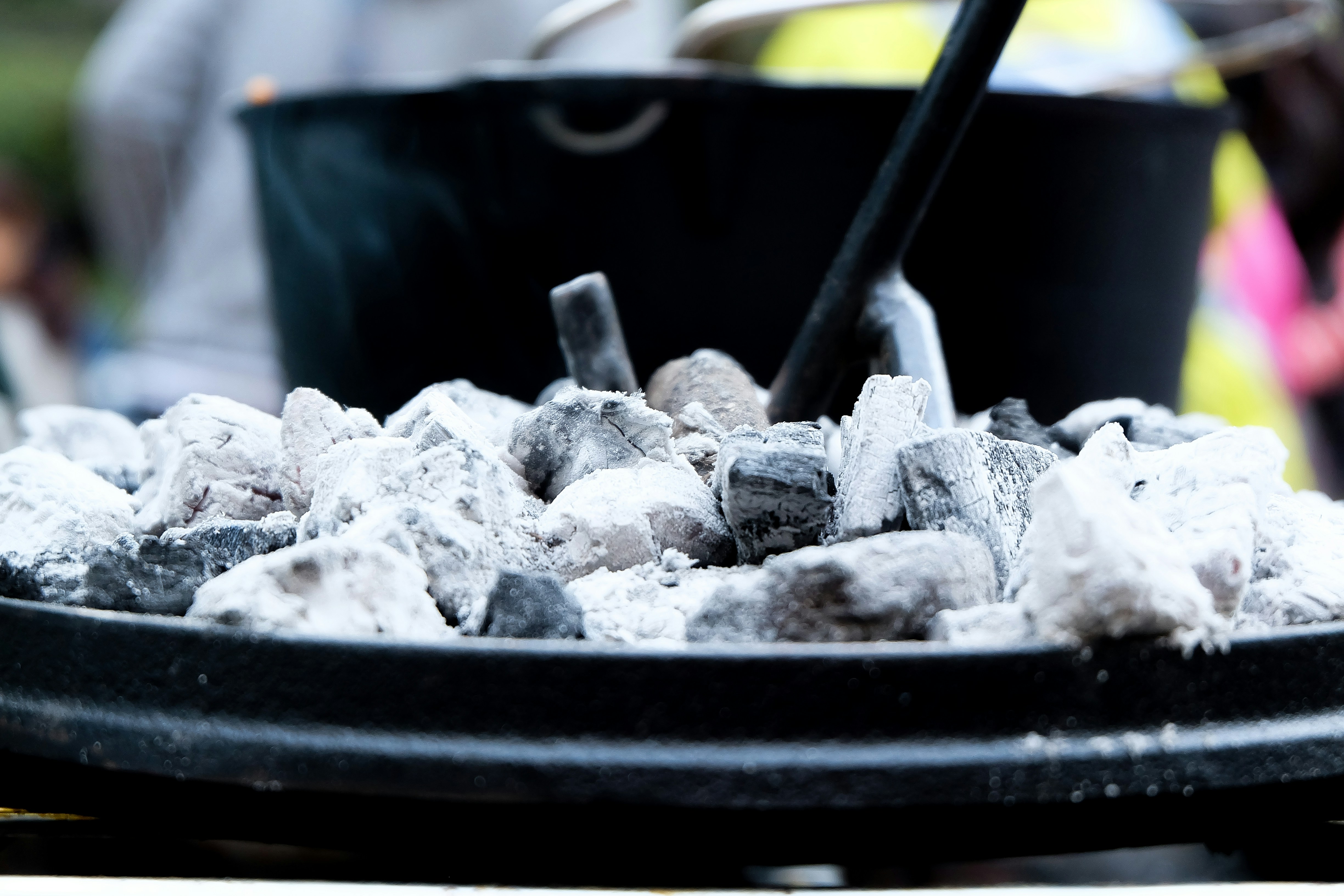 Close-up of gray charcoal briquettes in a grill, with a cooking pot in the background, ready for a culinary adventure.