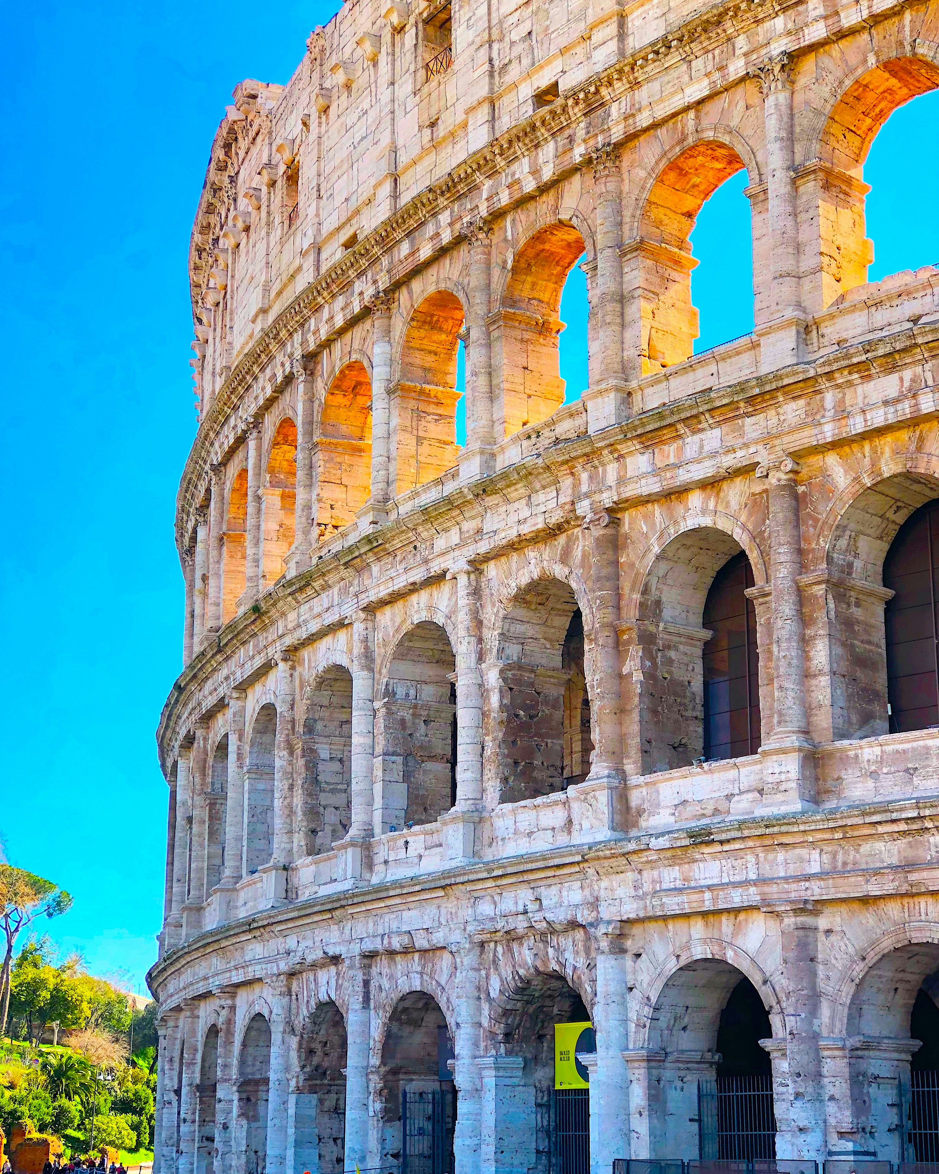 The Colosseum's majestic exterior showcases its iconic arches and weathered stone, framed by a vibrant blue sky.