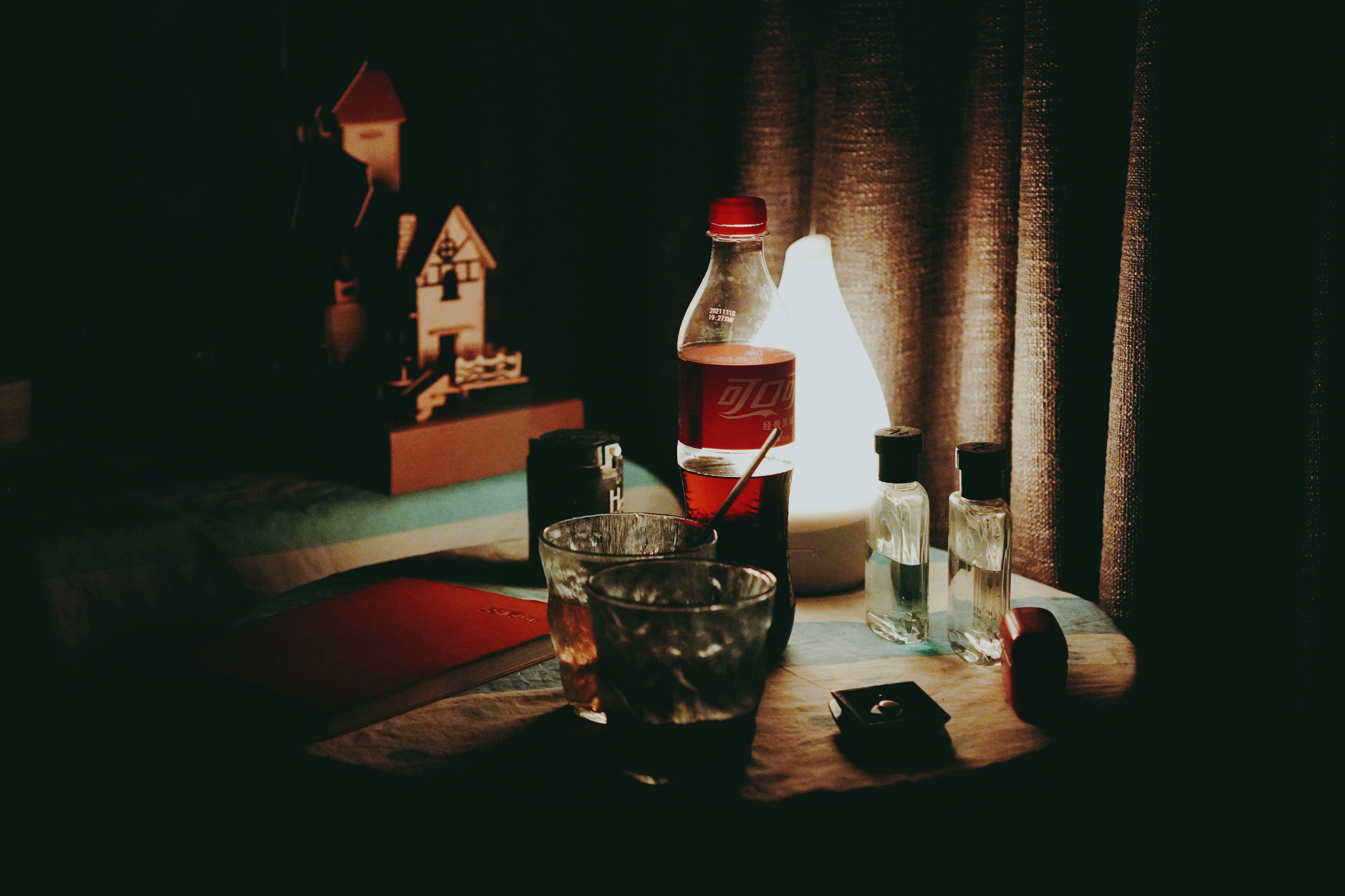 A cozy tabletop scene featuring a Coca-Cola bottle, glasses, and various perfume bottles illuminated by soft light, creating a warm atmosphere.