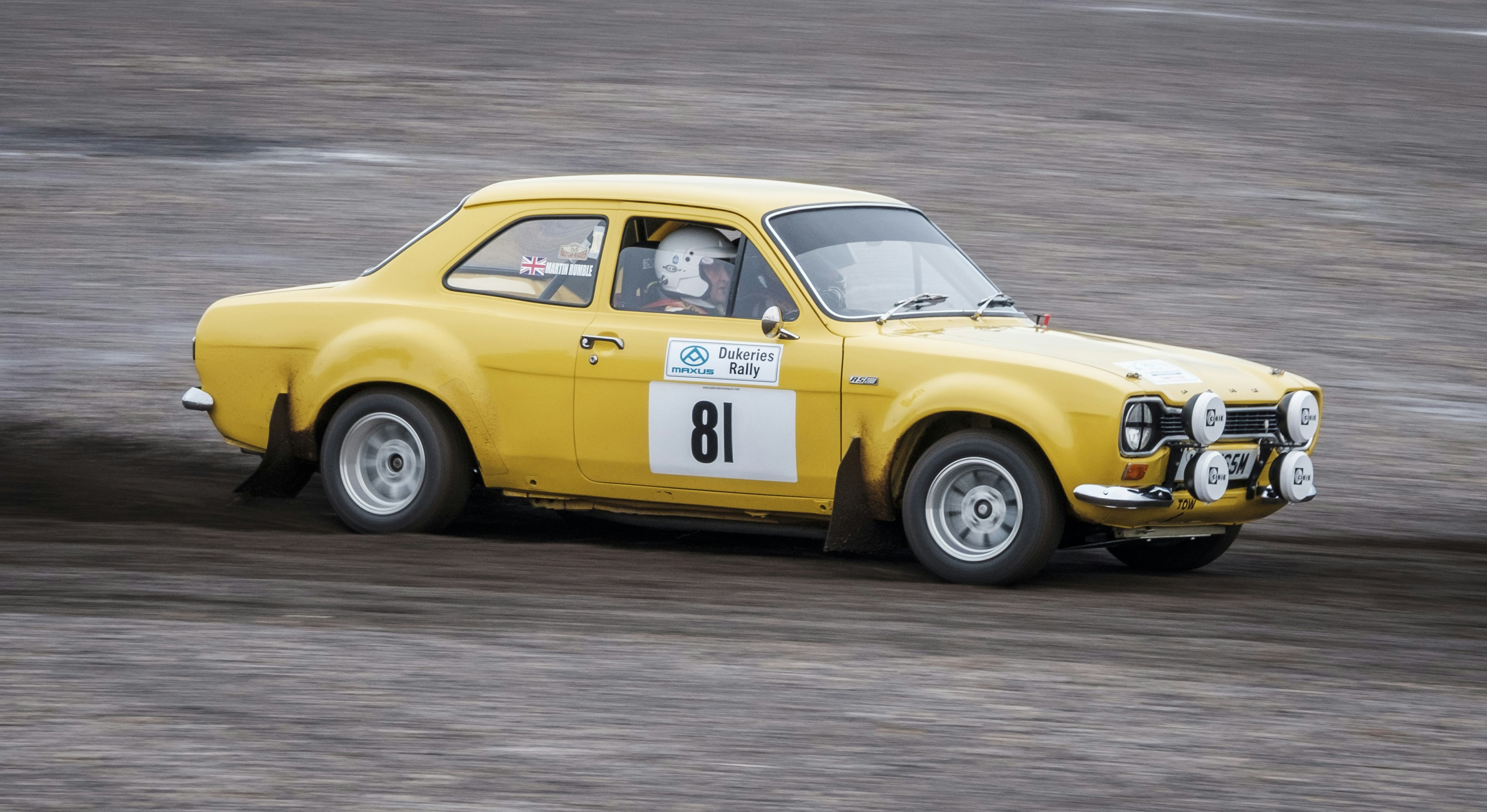 Classic yellow rally car drifting on a dirt track, showcasing its agility and speed during a race.