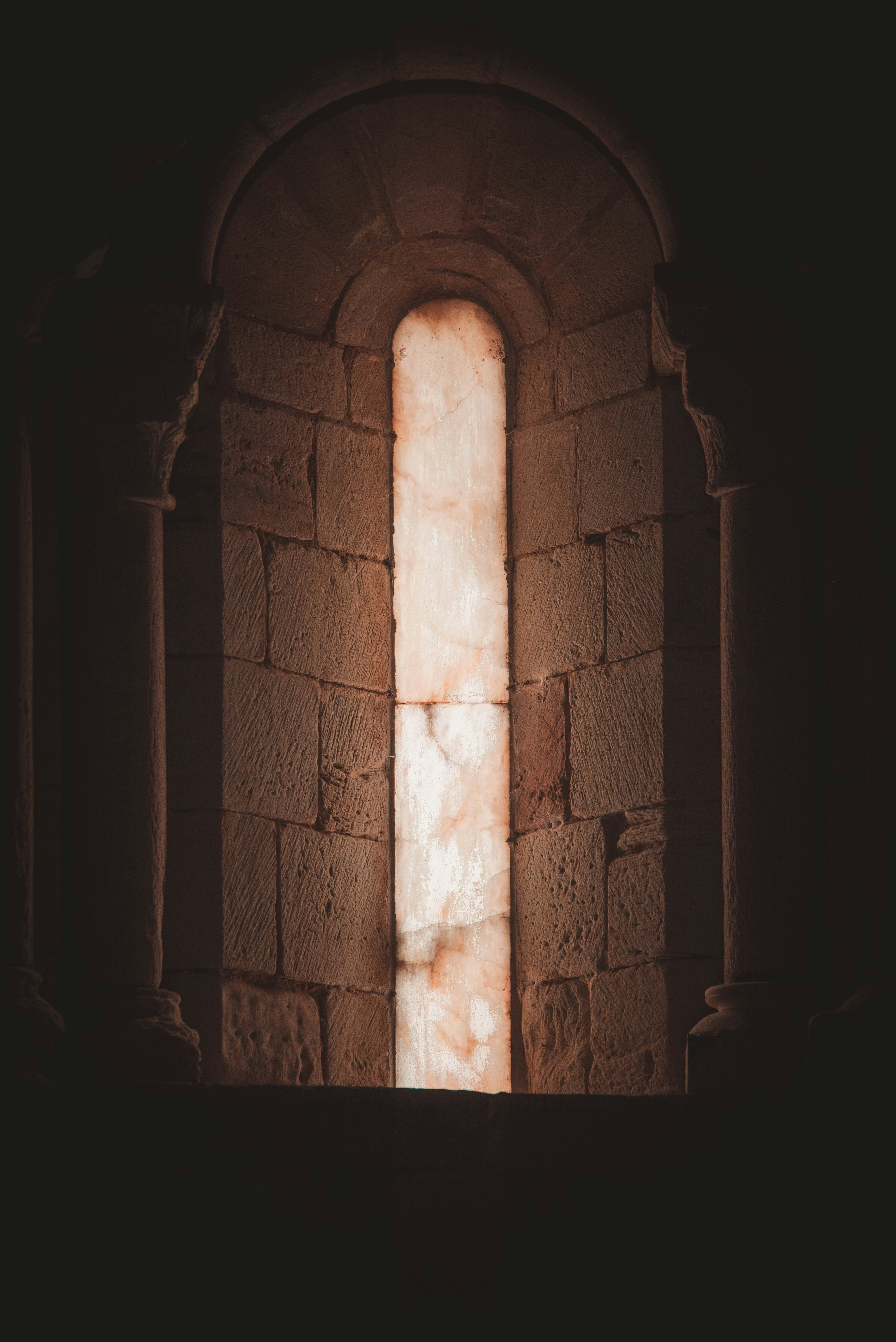 Translucent stone window framed by ancient columns, casting a soft glow in a dimly lit space.