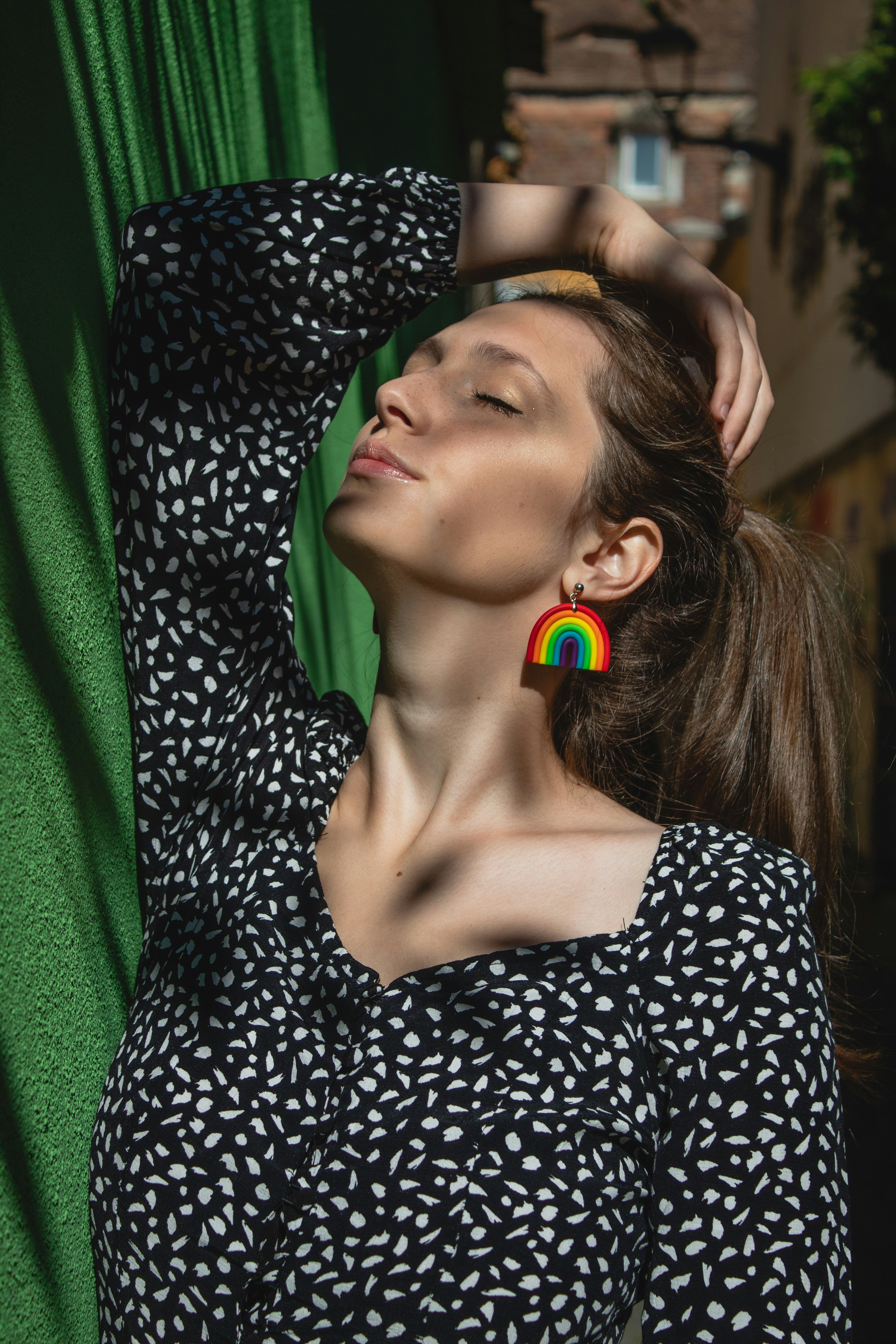 Sunlit Profile: Rainbow Earrings Framed by a Velvet Green Curtain