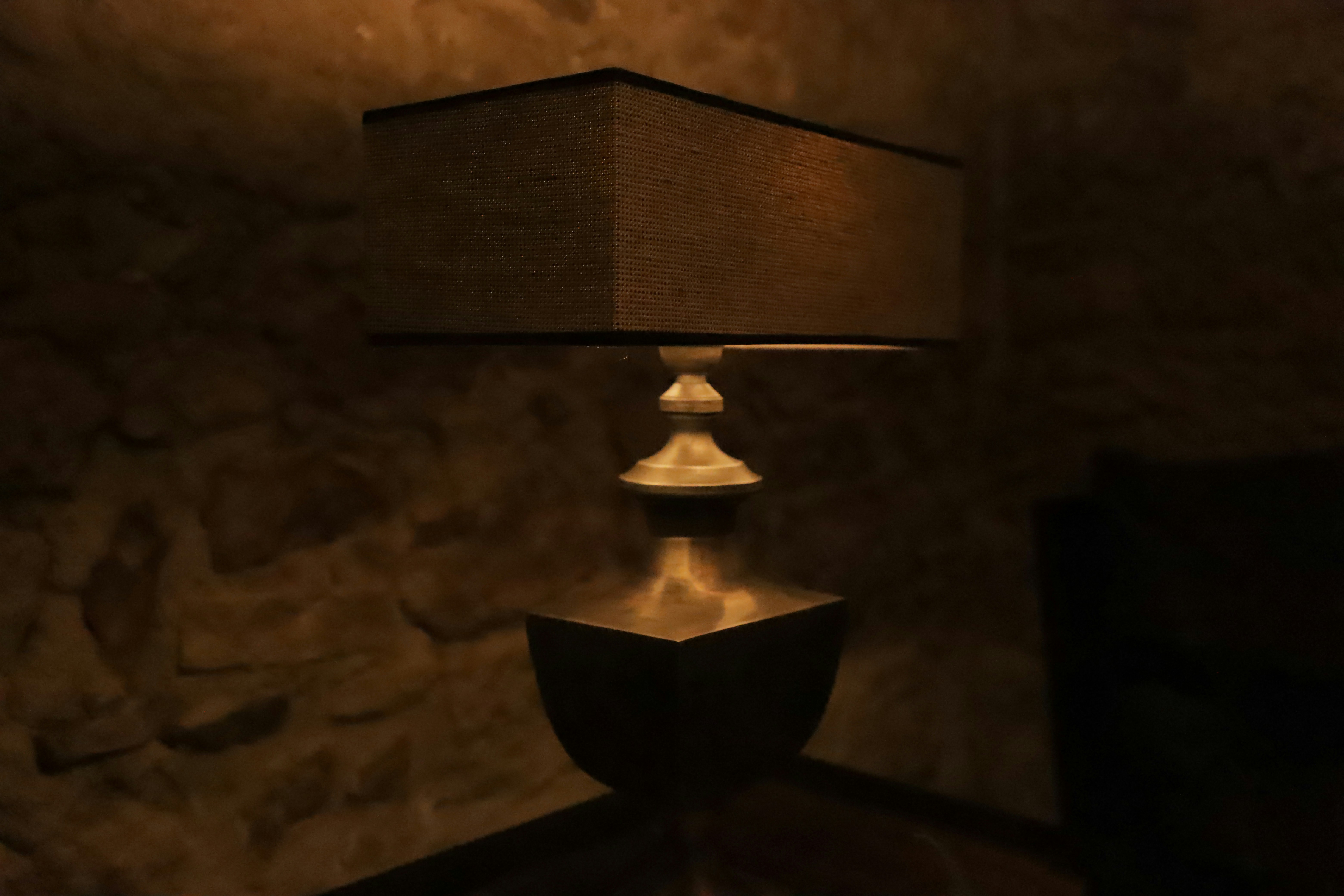 A vintage lamp casts a warm glow against a rustic stone wall, creating a cozy atmosphere in a dimly lit space.