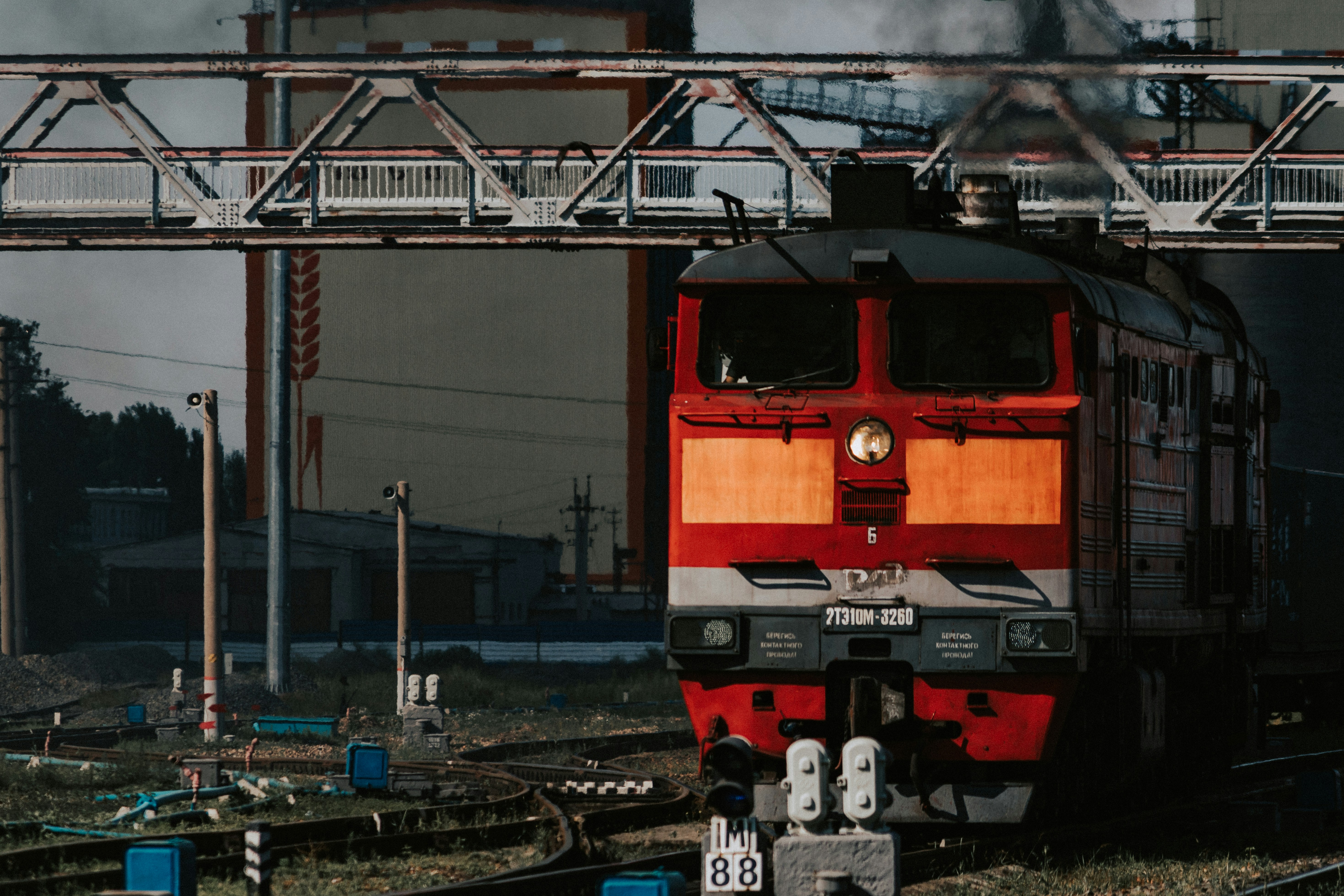 Iron Span Encounter: A Red Locomotive under the Rail Yard Overpass