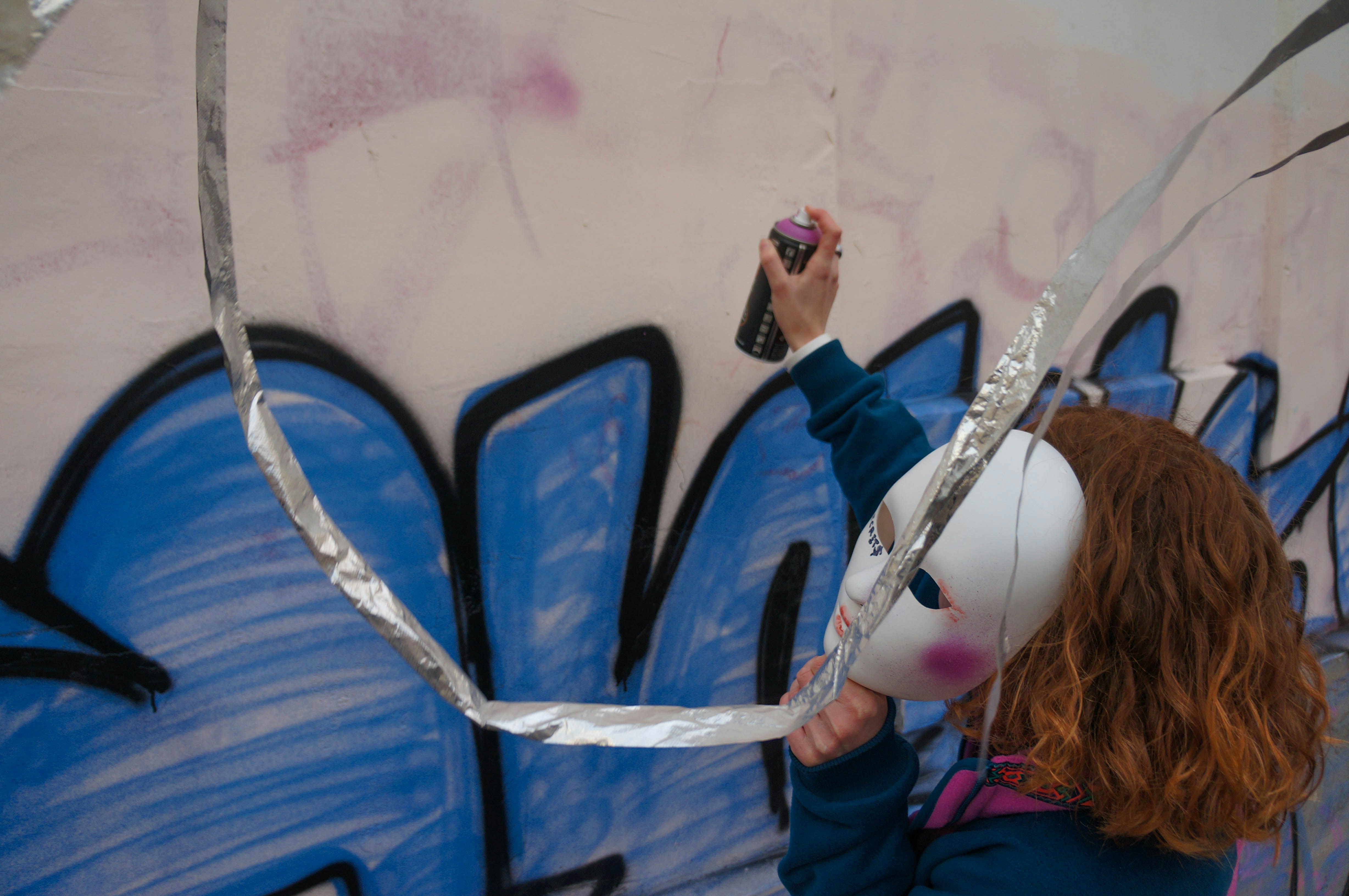 Masked Sprayer in Front of Blue Graffiti: A Quiet Urban Moment