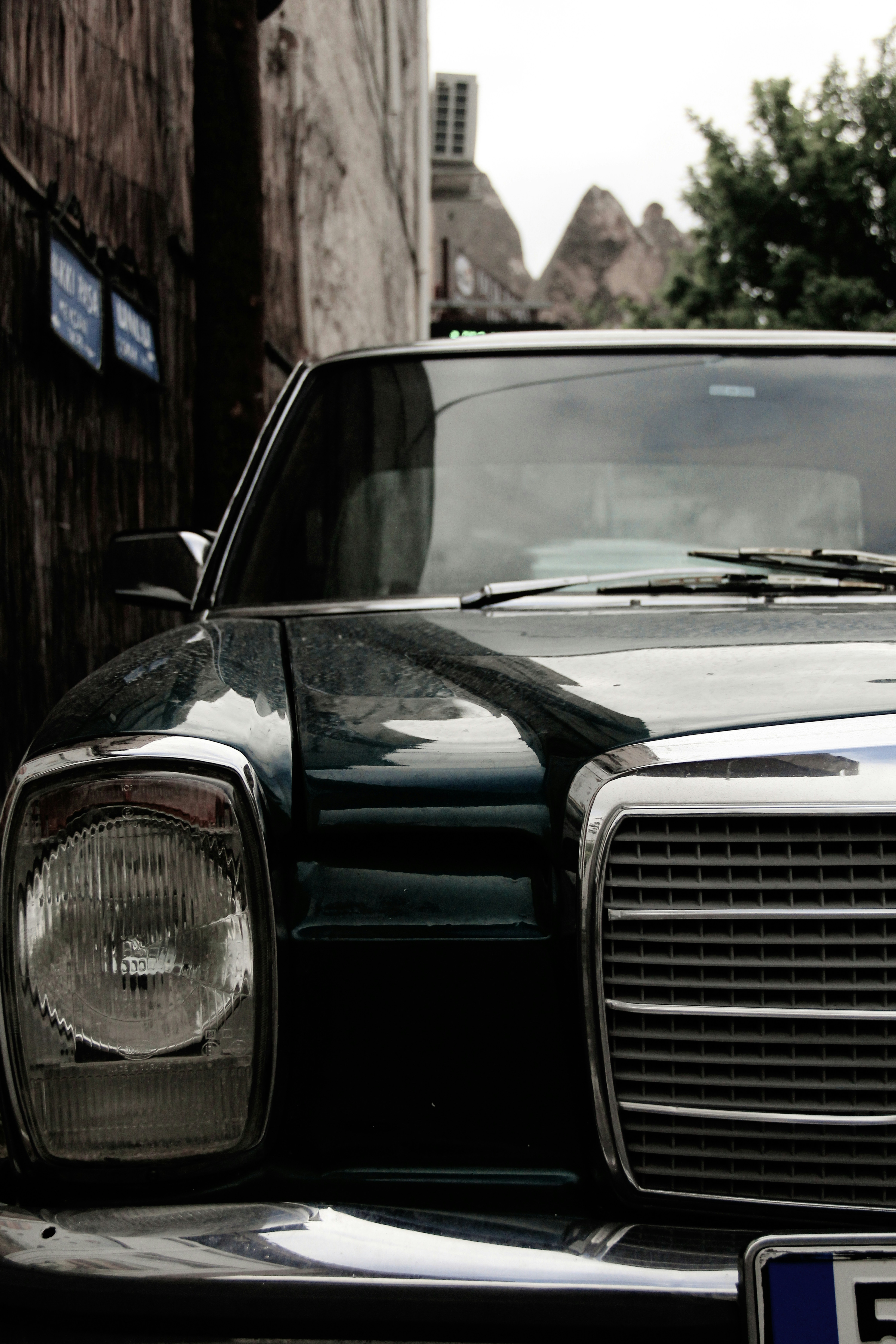 Close-up of a vintage car's front, showcasing its intricate details and reflections against an urban backdrop.