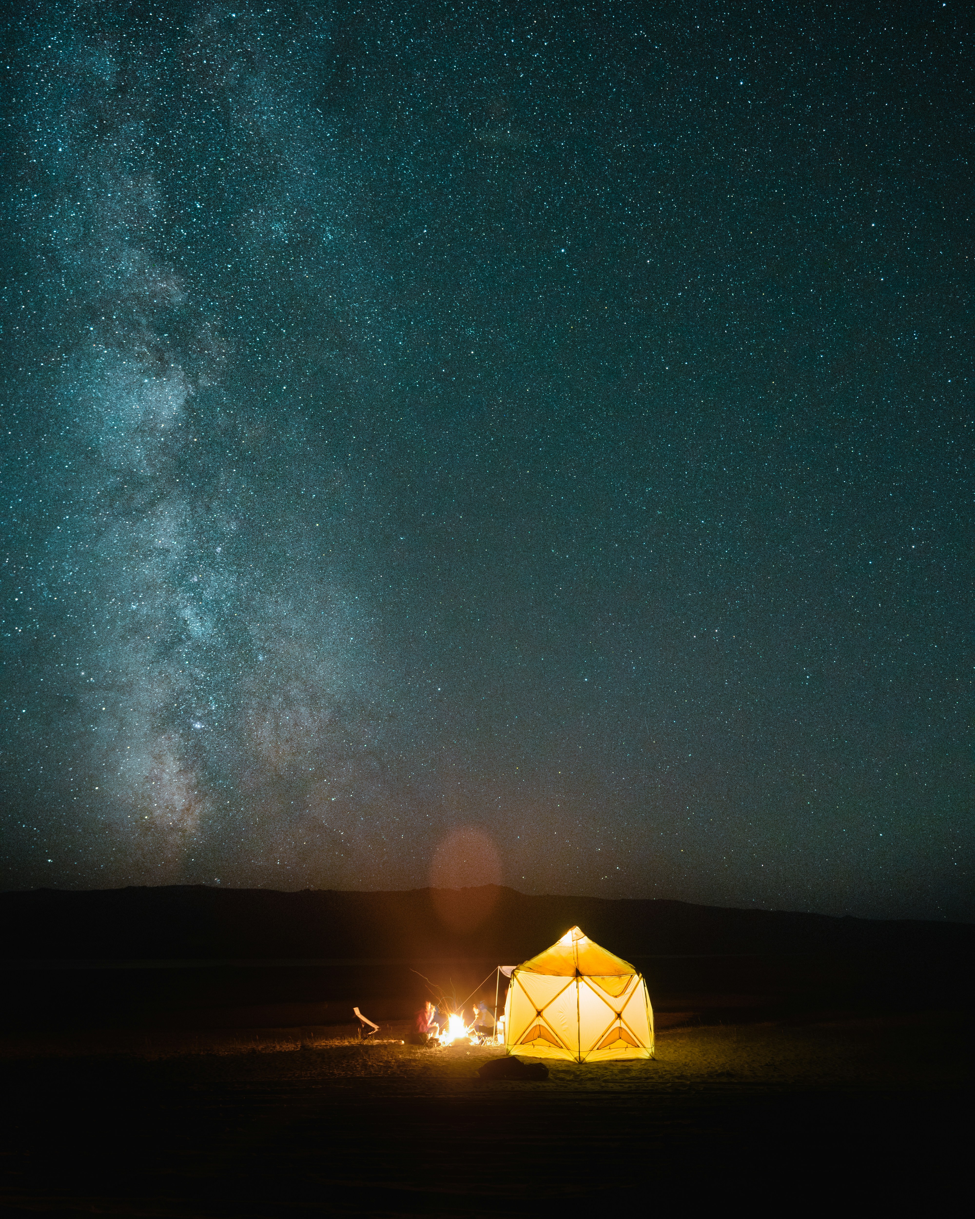 A vibrant tent illuminated by a campfire beneath a sprawling starry sky, showcasing the Milky Way's brilliance.