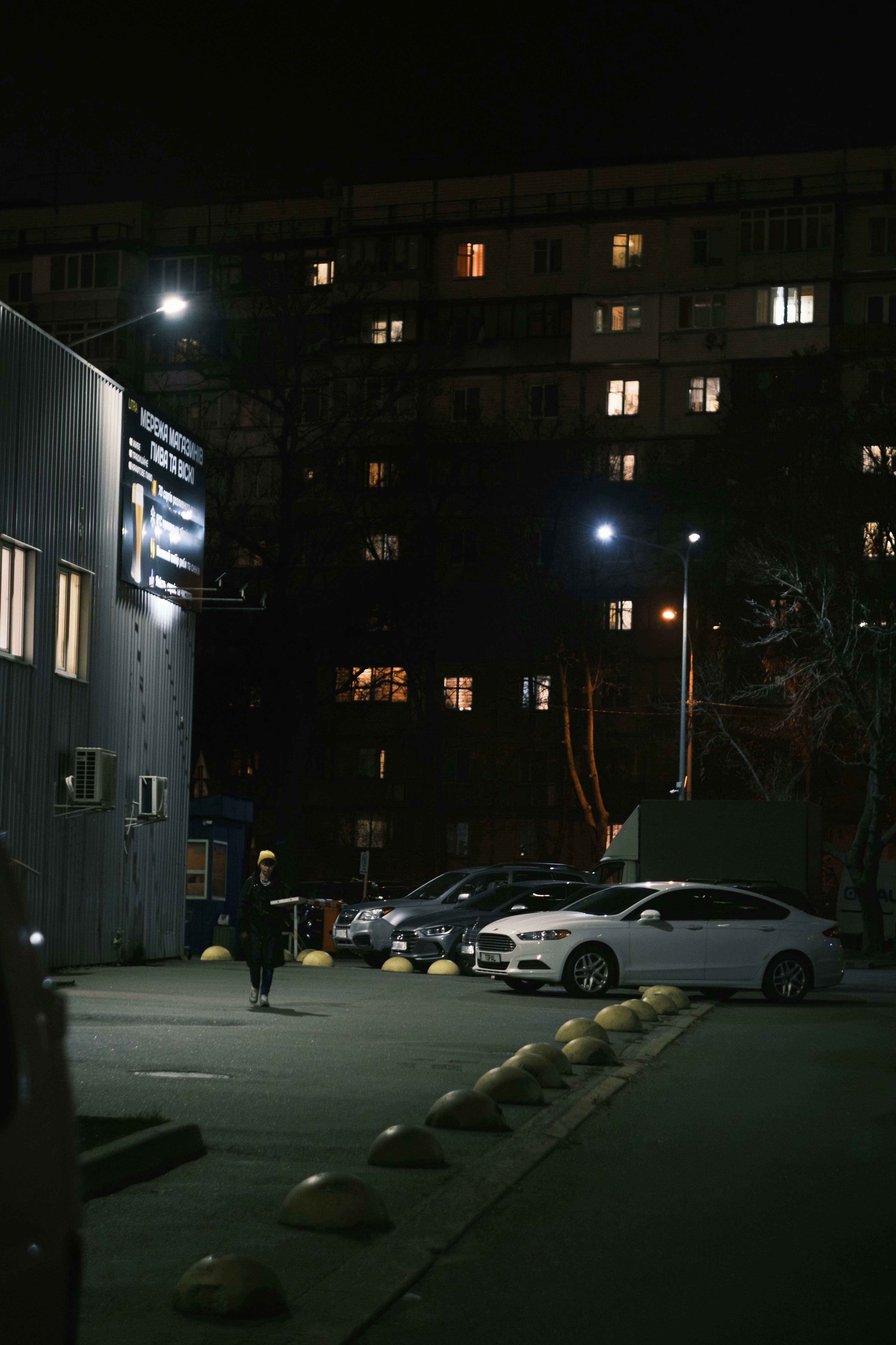 Lone Pedestrian Under Streetlight in a Night Parking Lot