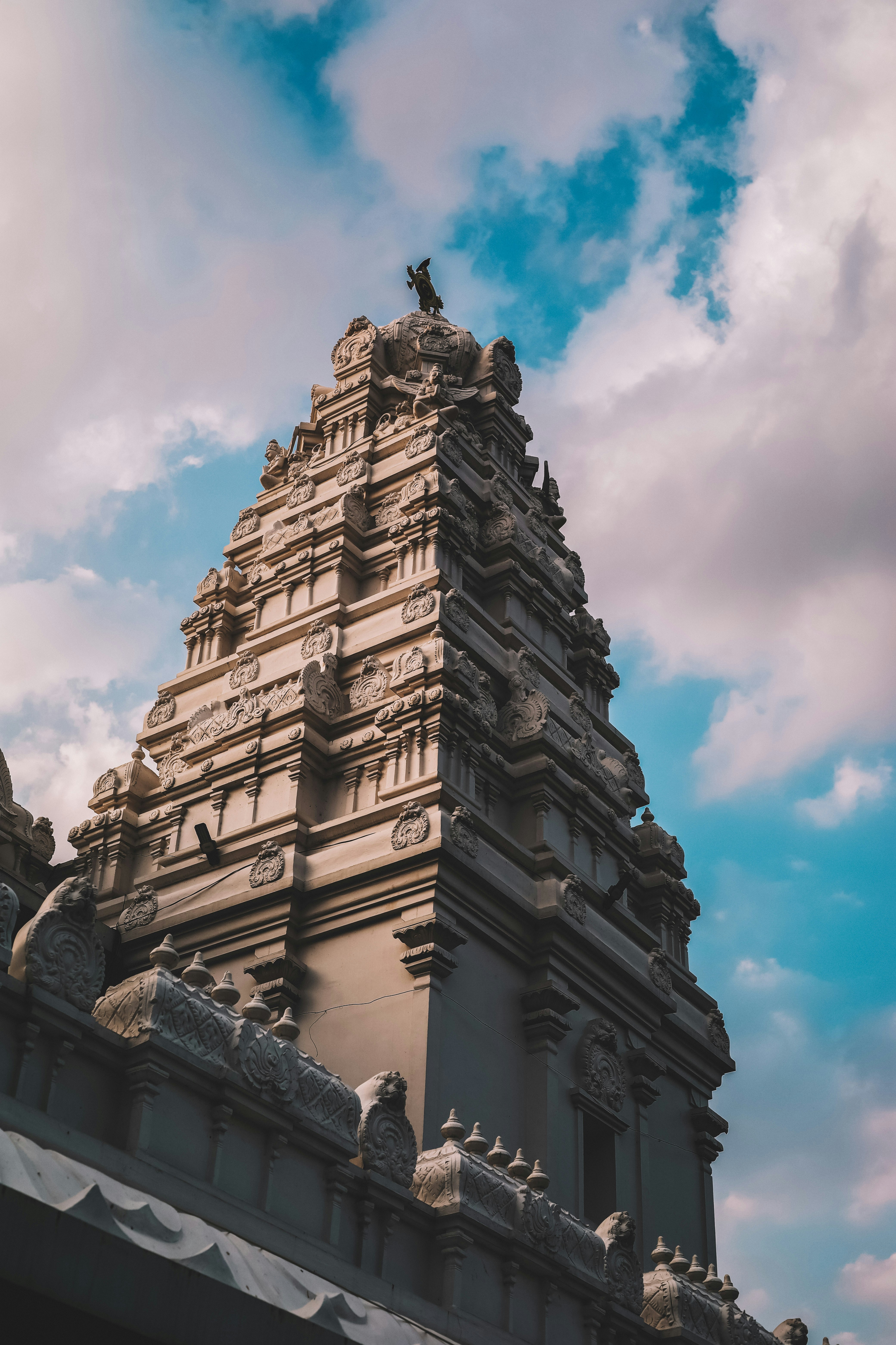 Intricately carved temple spire reaching towards the sky, framed by dynamic clouds. A symbol of architectural grandeur.
