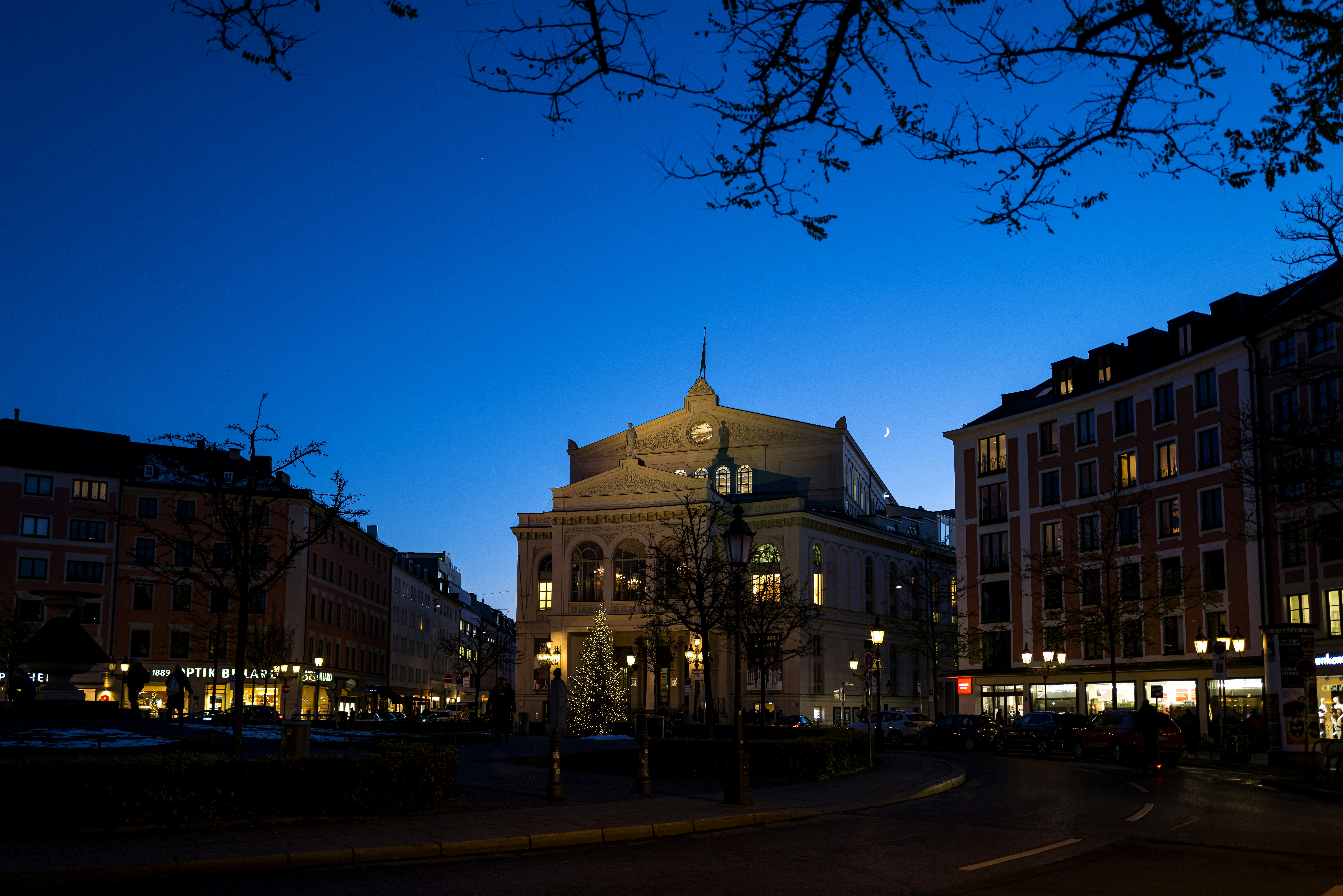 Historic theater illuminated against a deep blue twilight sky, surrounded by urban architecture and festive decorations.
