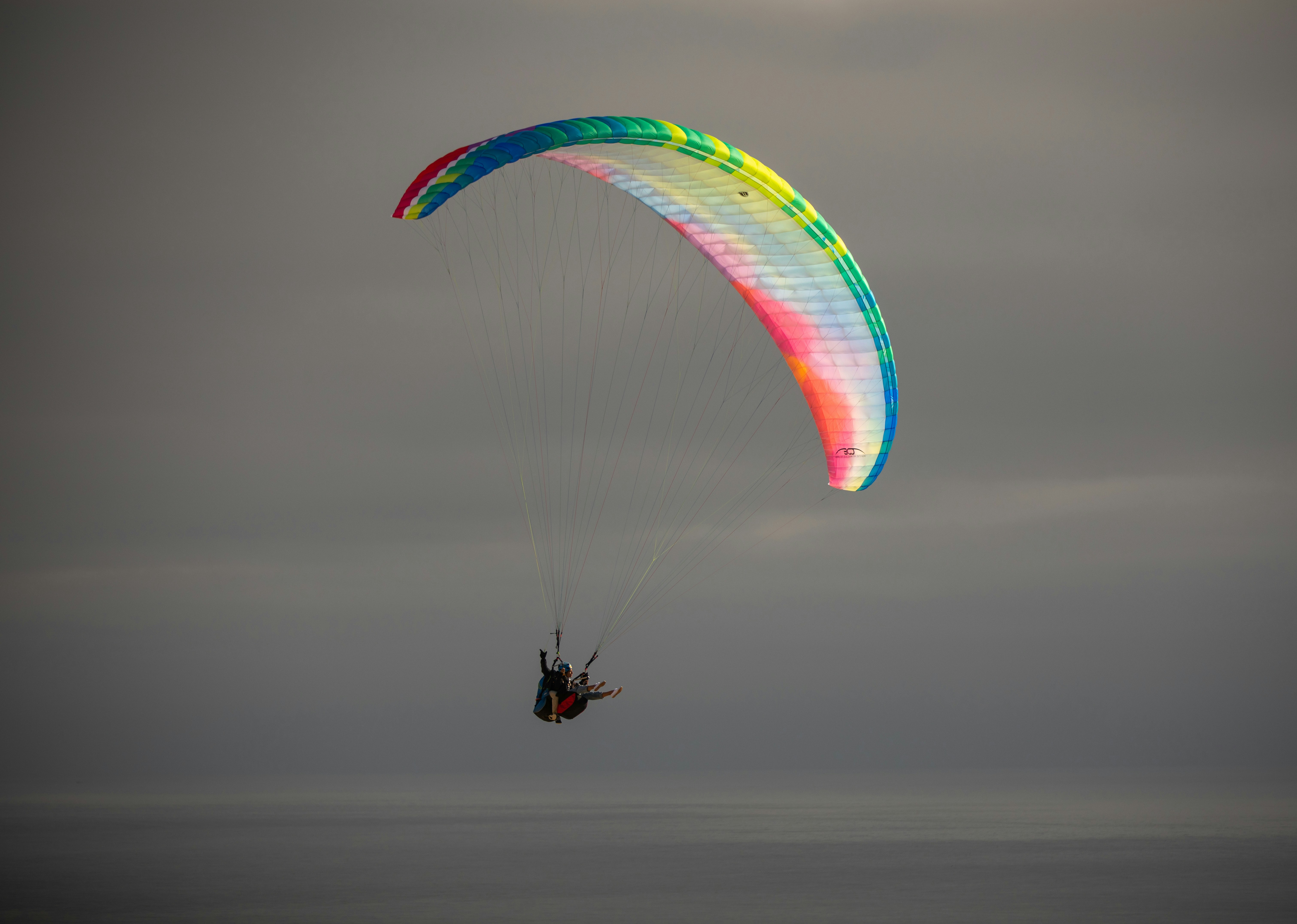 A little color on a gray day | a person is parasailing in the ocean on a cloudy day