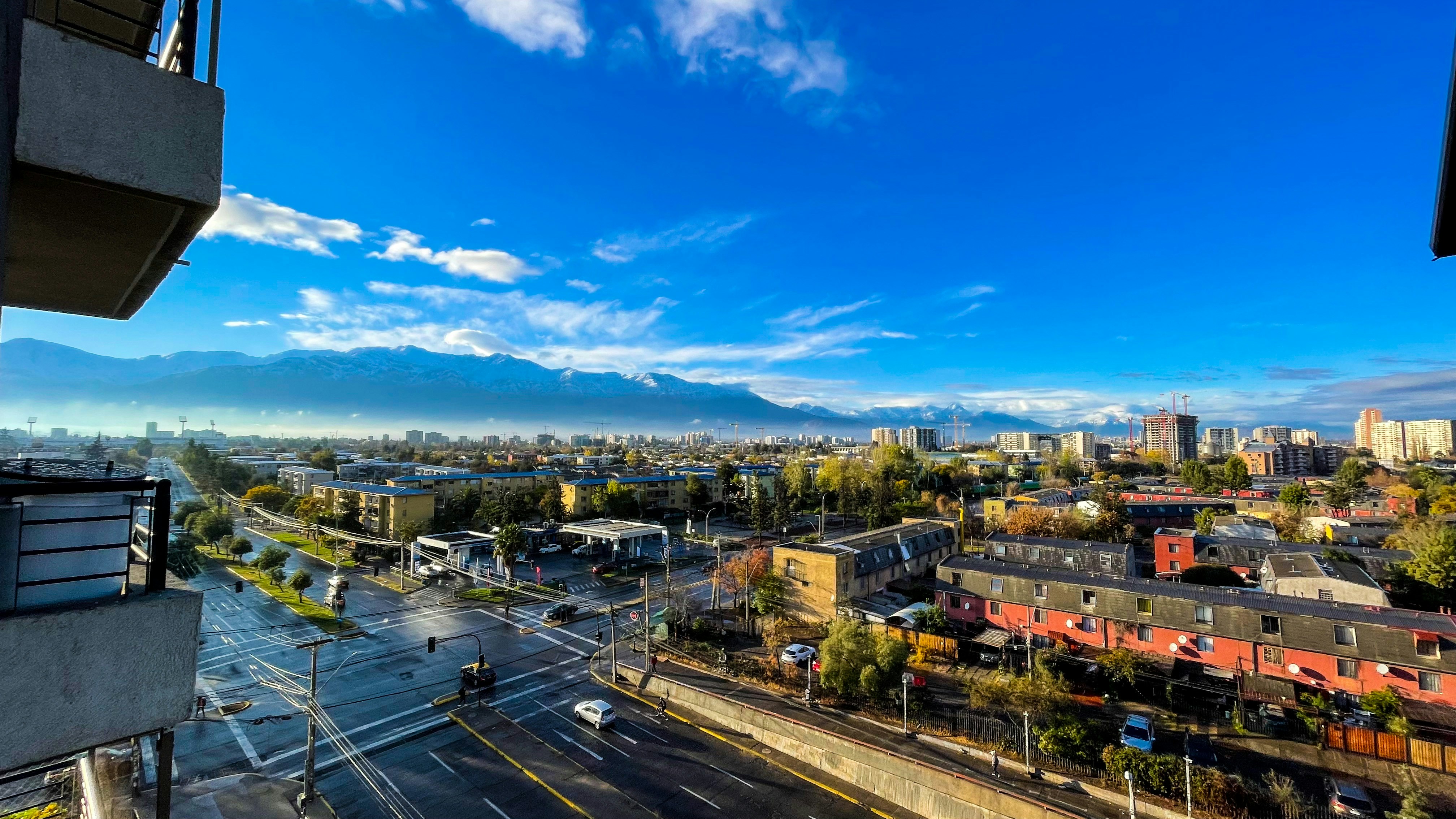 Cityscape with vibrant buildings and roads leading to distant mountains under a clear blue sky.