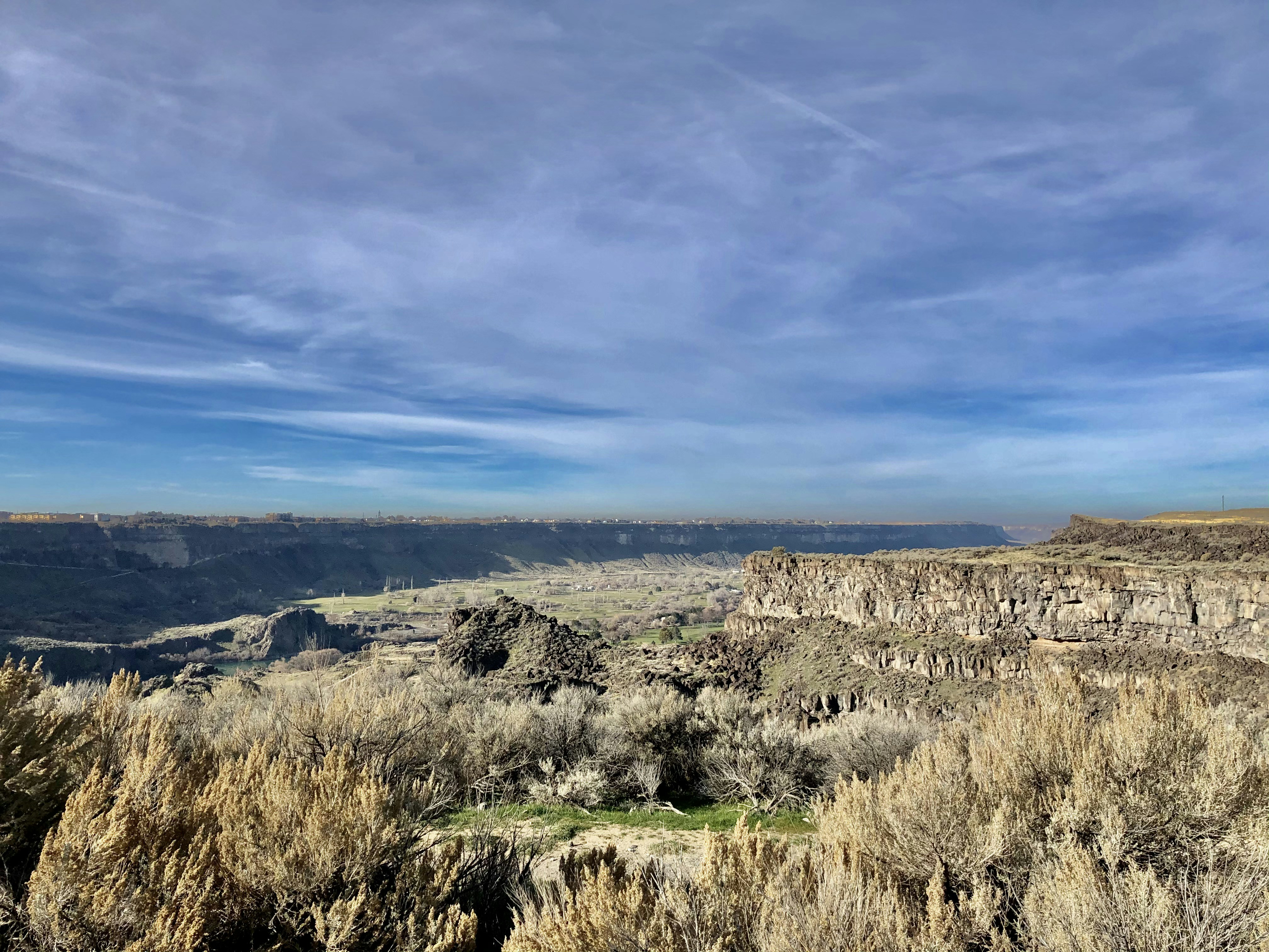 Vast canyon landscape with rugged cliffs and sparse vegetation under a clear blue sky. The scene captures the tranquility of nature's raw beauty.
