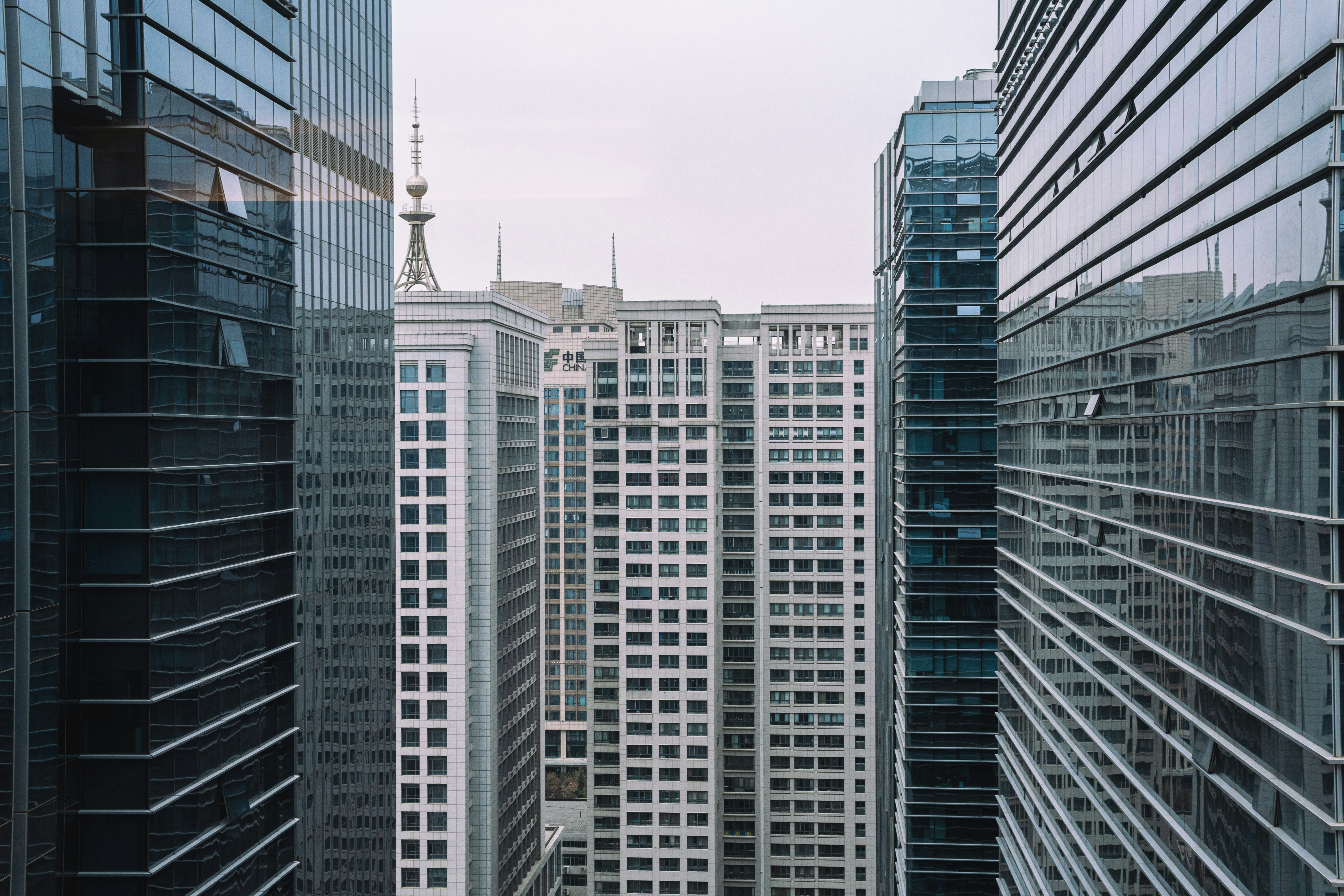 Cluster of skyscrapers with reflective glass facades under an overcast sky.