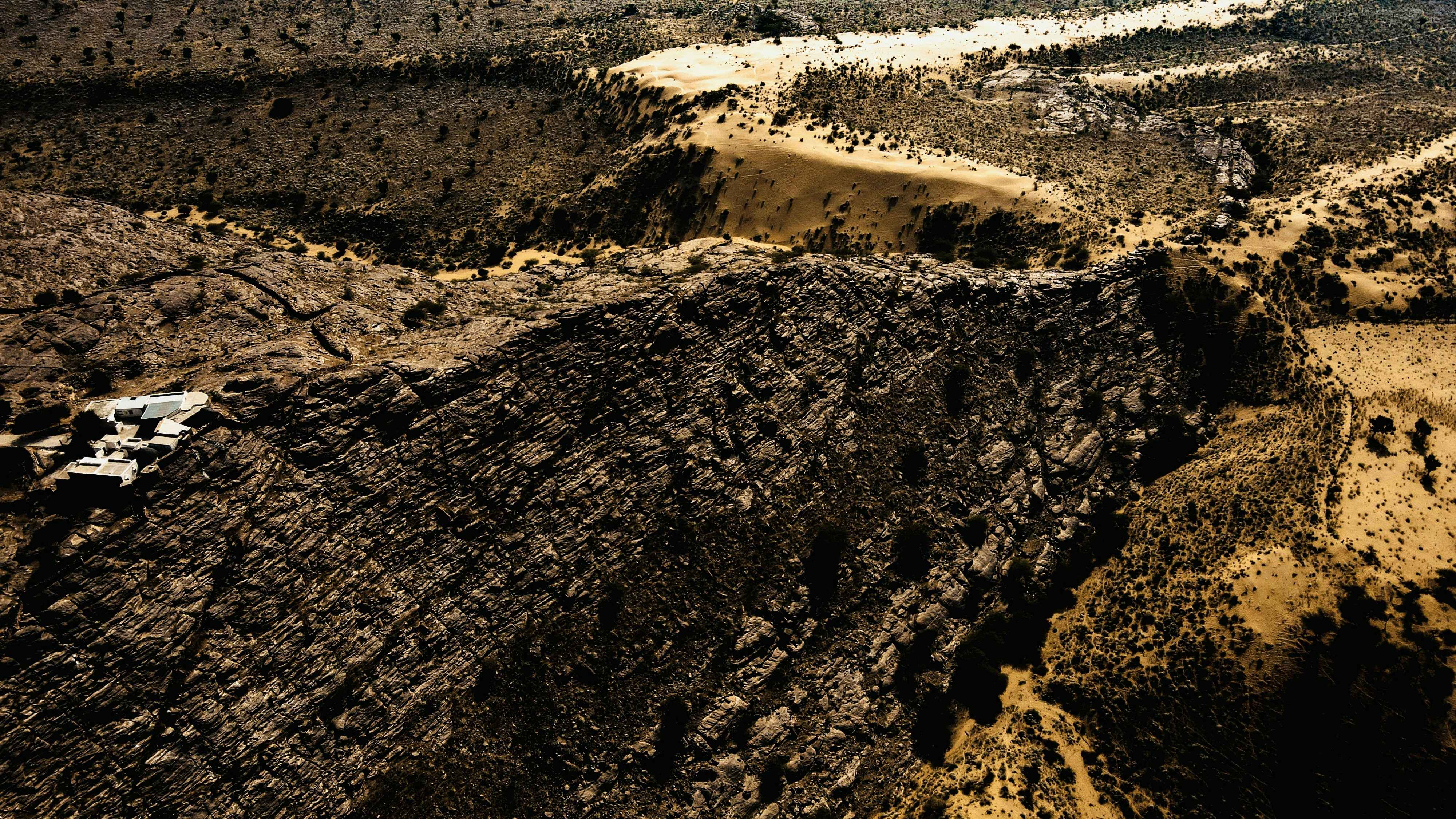 Aerial view of a rugged terrain showcasing dramatic rock formations and contrasting sandy areas, highlighting the effects of erosion over time.