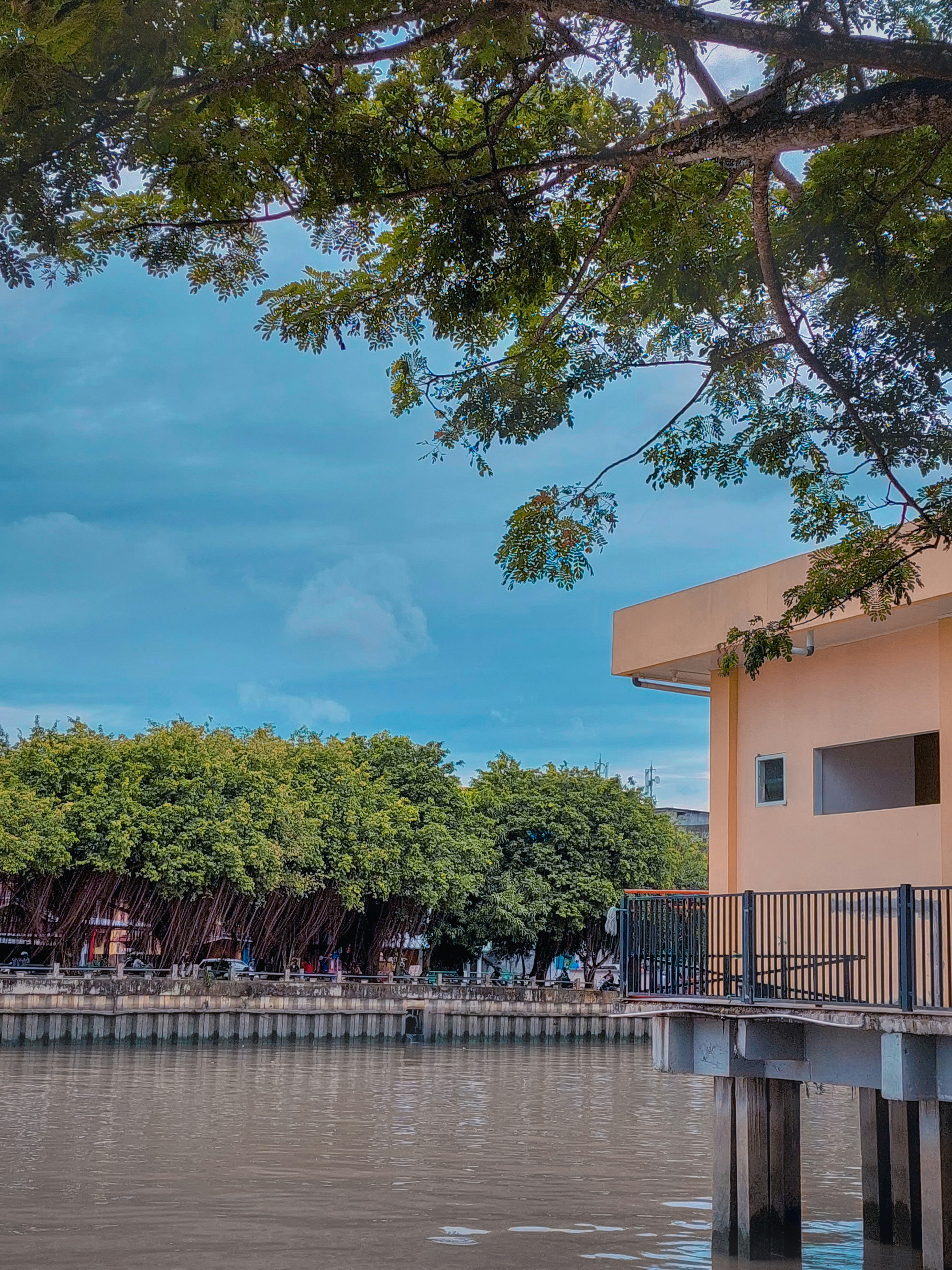 Modern building overhanging a calm river with lush green trees and a bright blue sky.