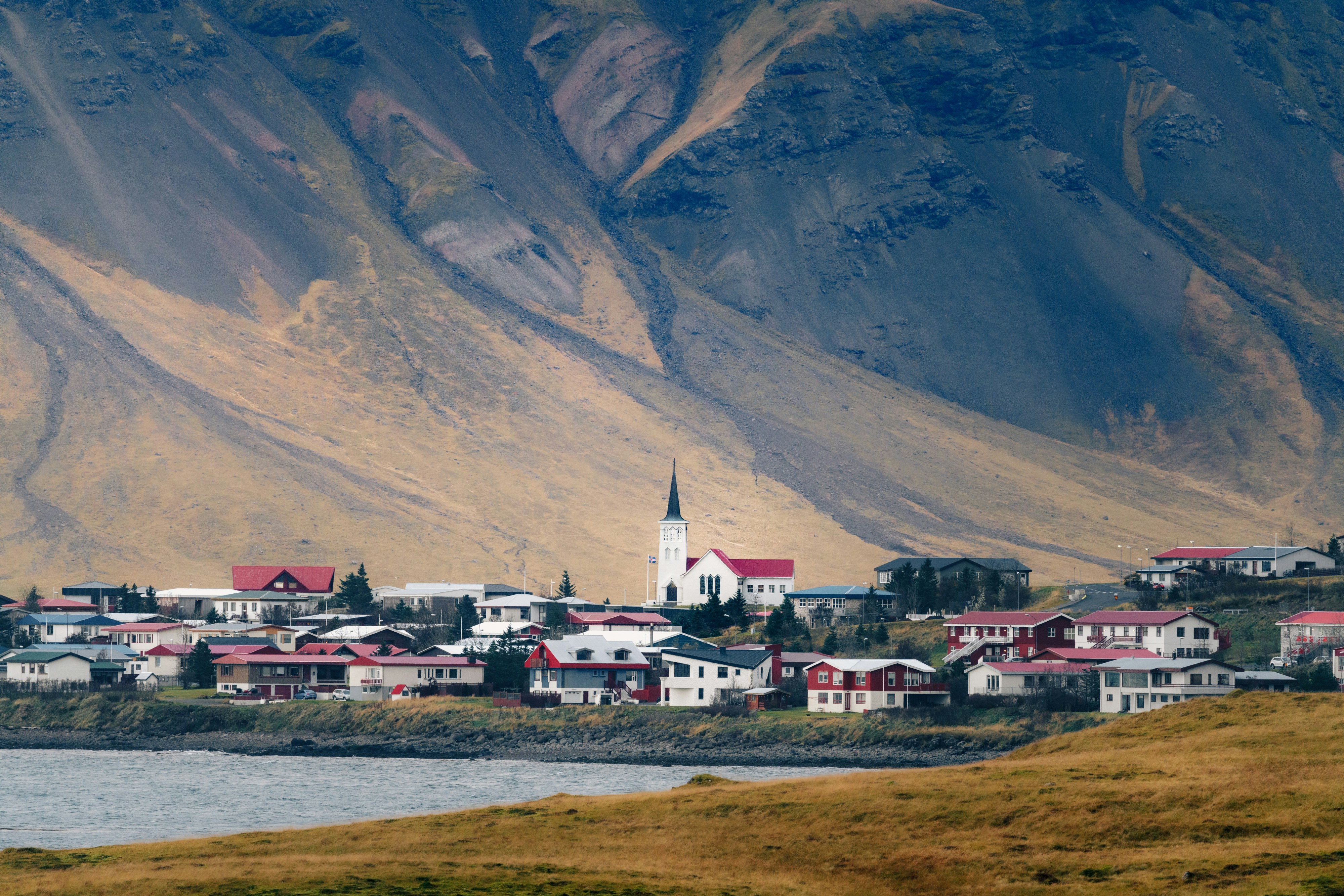 Steeple Amid Red Roofs: A Coastal Village Framed by Majestic Peaks