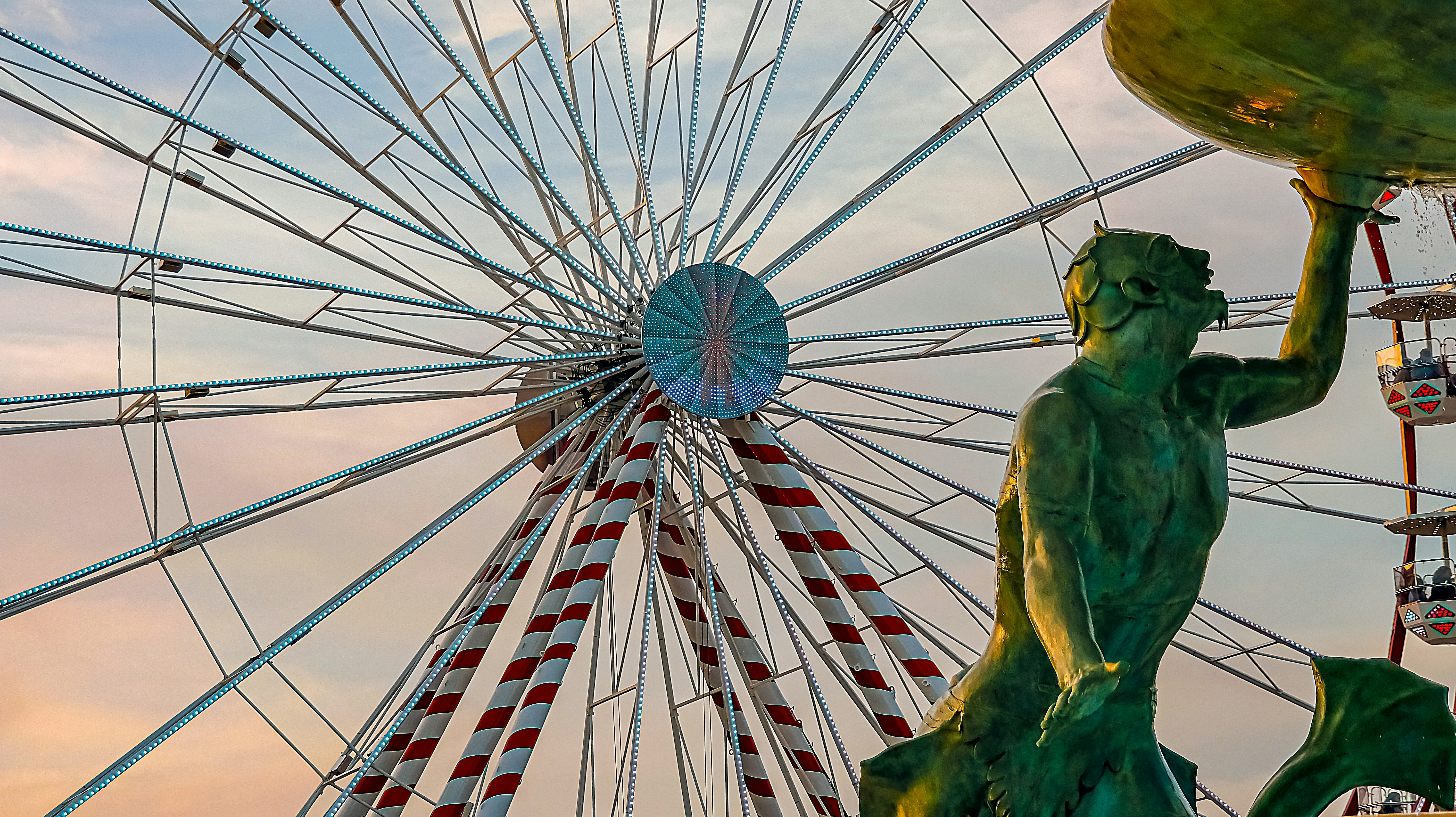 Ferris Wheel Hub at Sunset Framed by a Verdant Statue