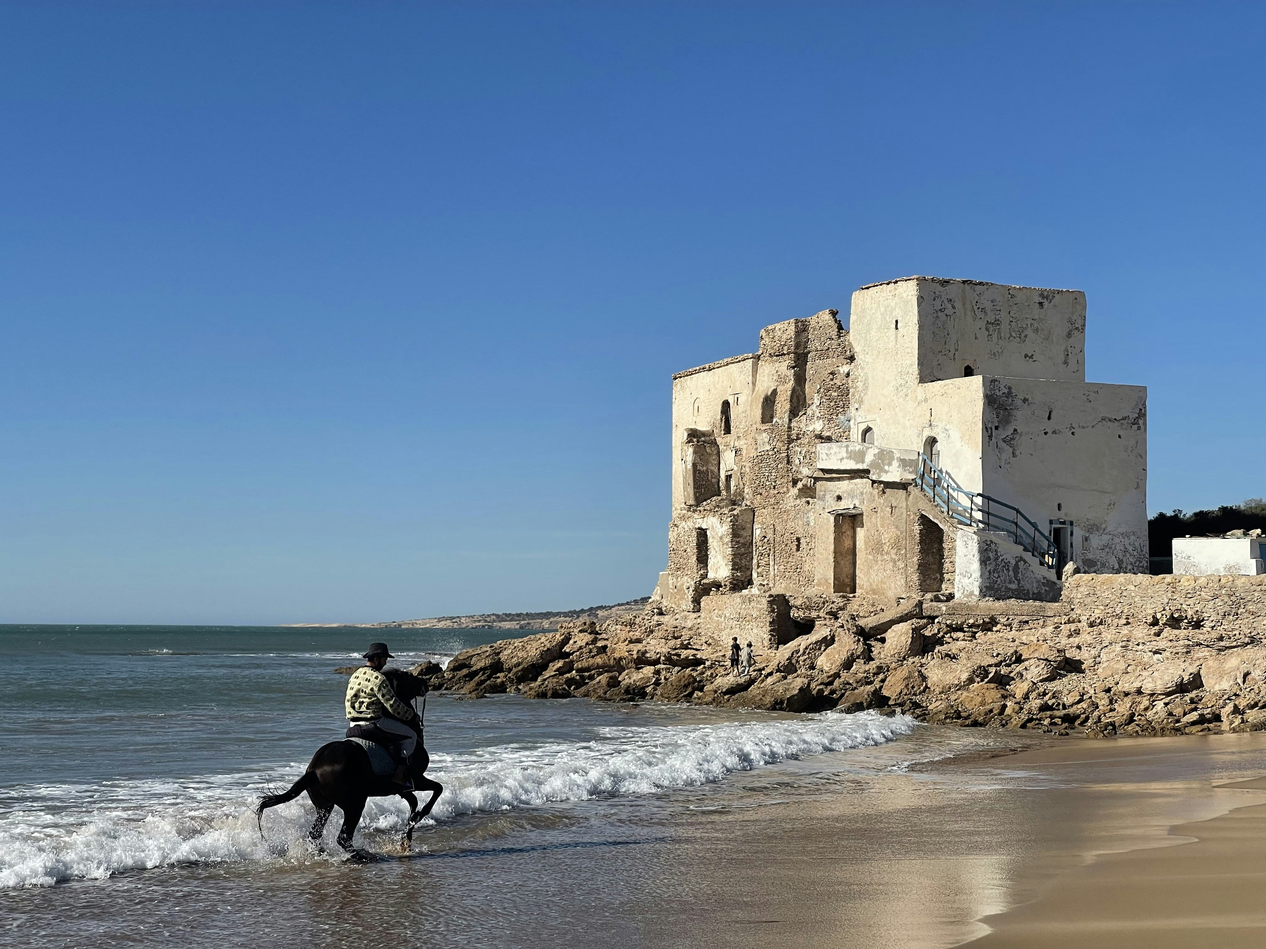 a man riding a horse on a beach next to the ocean