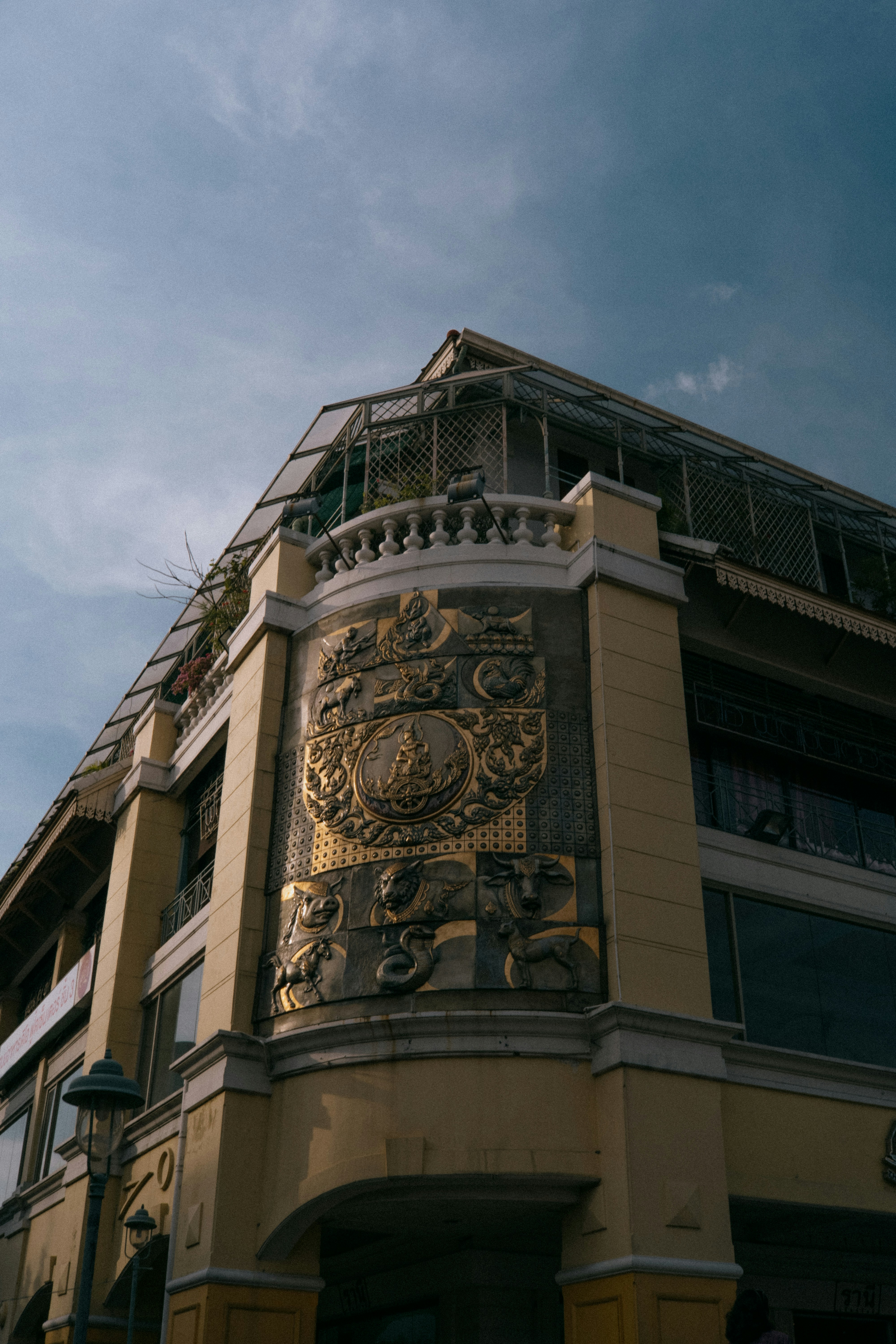 Photograph of a yellow building corner featuring a prominent bronze crest relief and decorative balconies against a clear blue sky.
