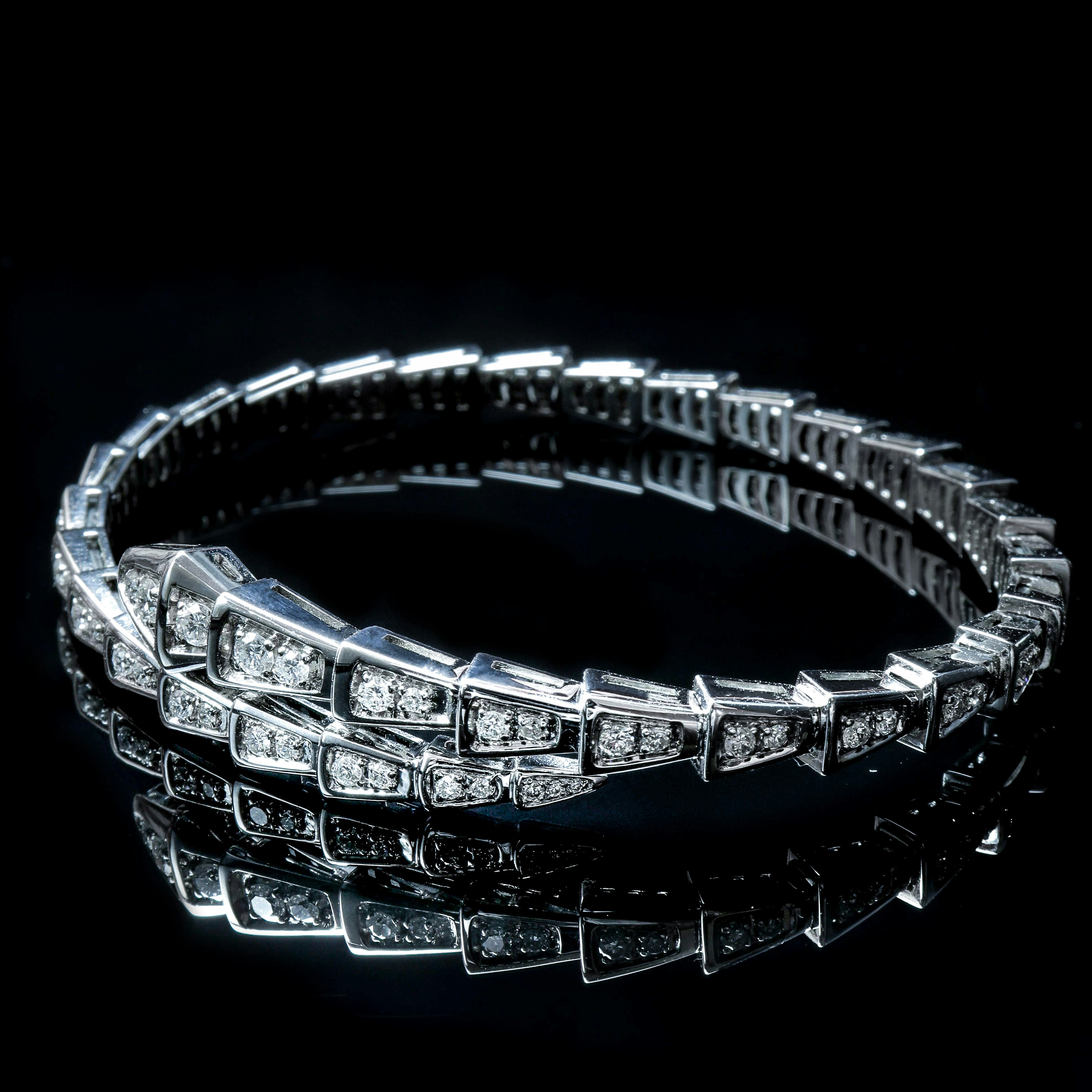 Intricately designed silver bracelet adorned with sparkling stones, reflecting light against a dark backdrop.