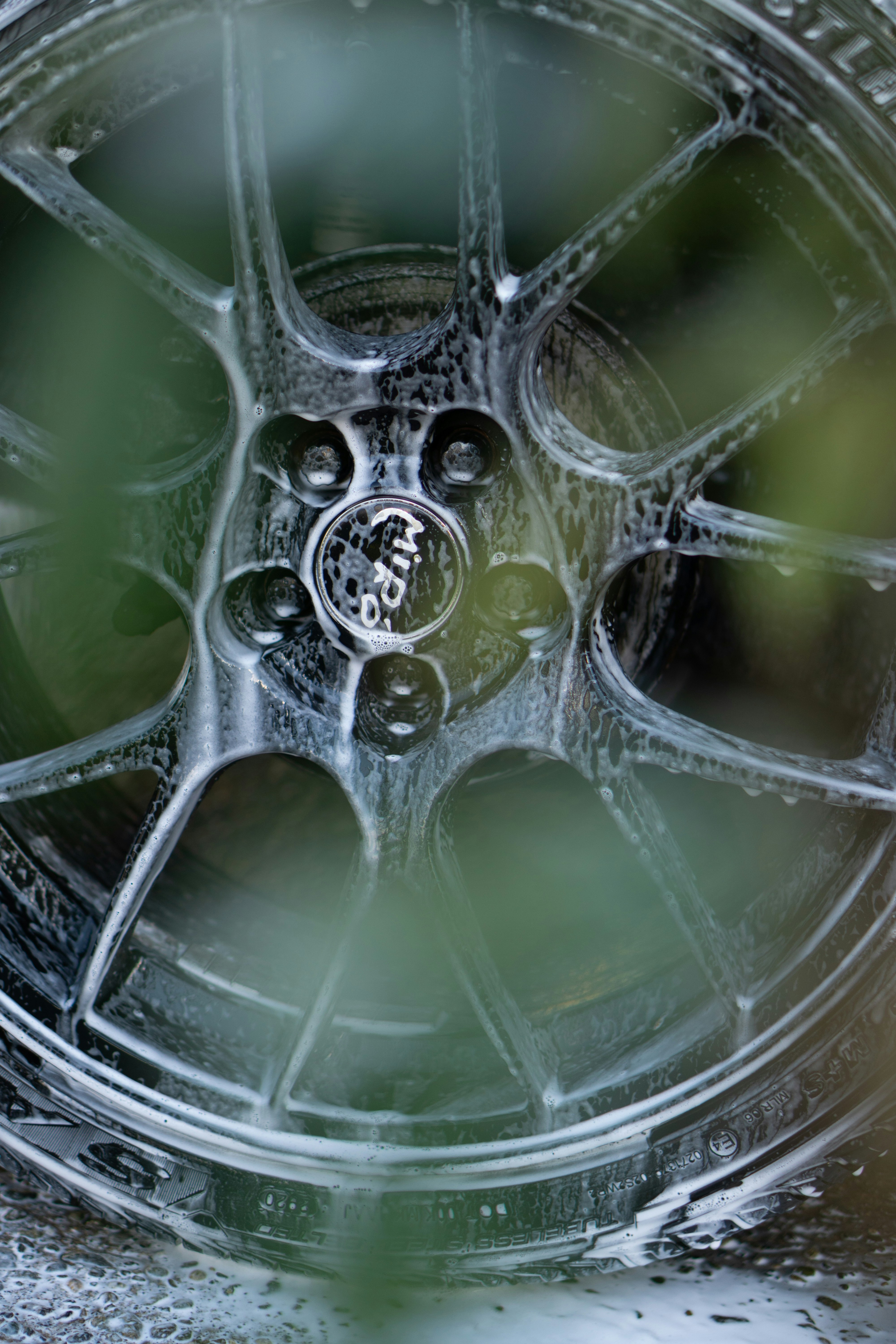 Rain-Kissed Spokes: a macro study of a wet alloy wheel framed by emerald bokeh