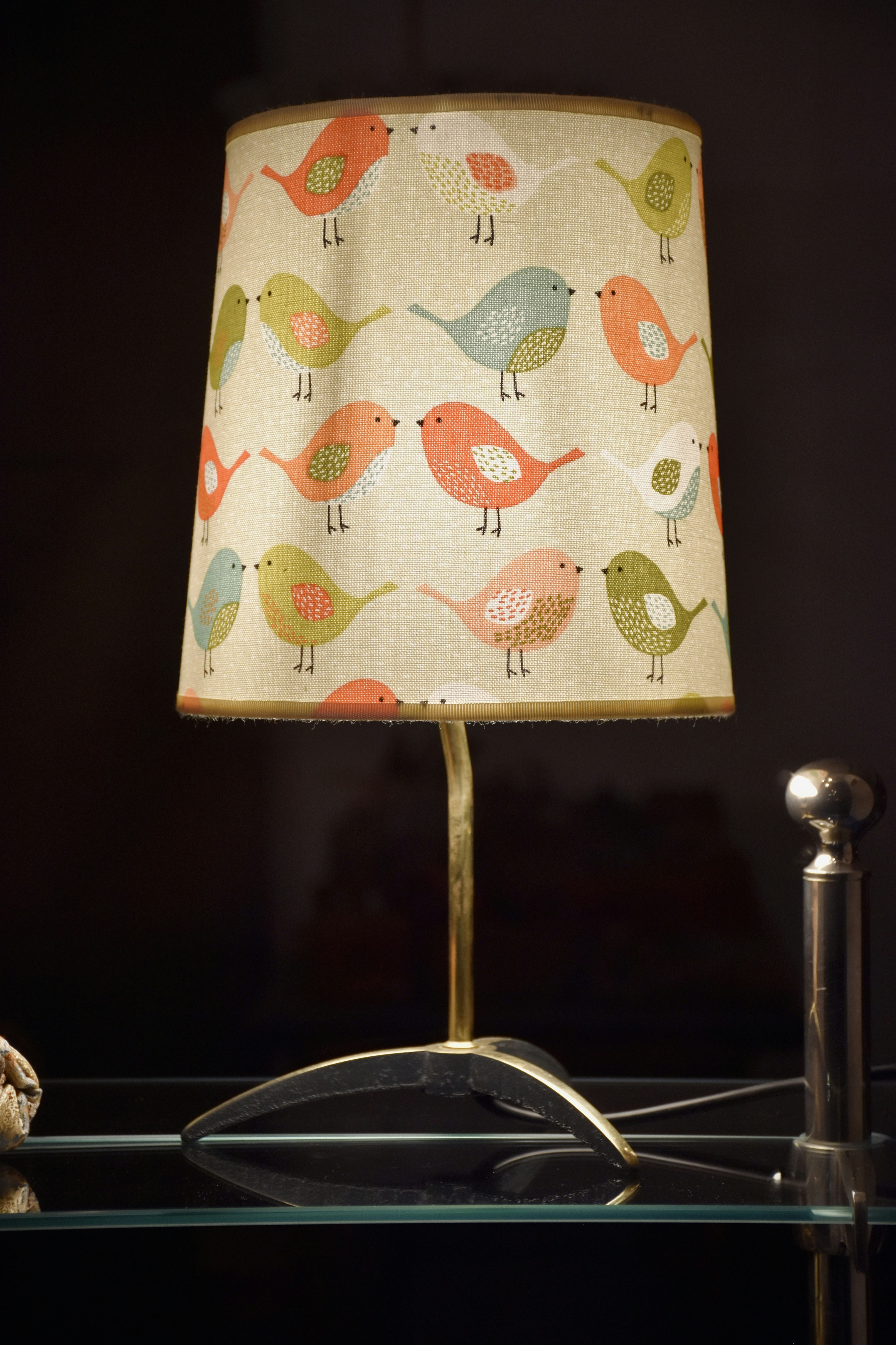 A charming lamp adorned with colorful bird illustrations, casting a warm glow in a cozy setting.