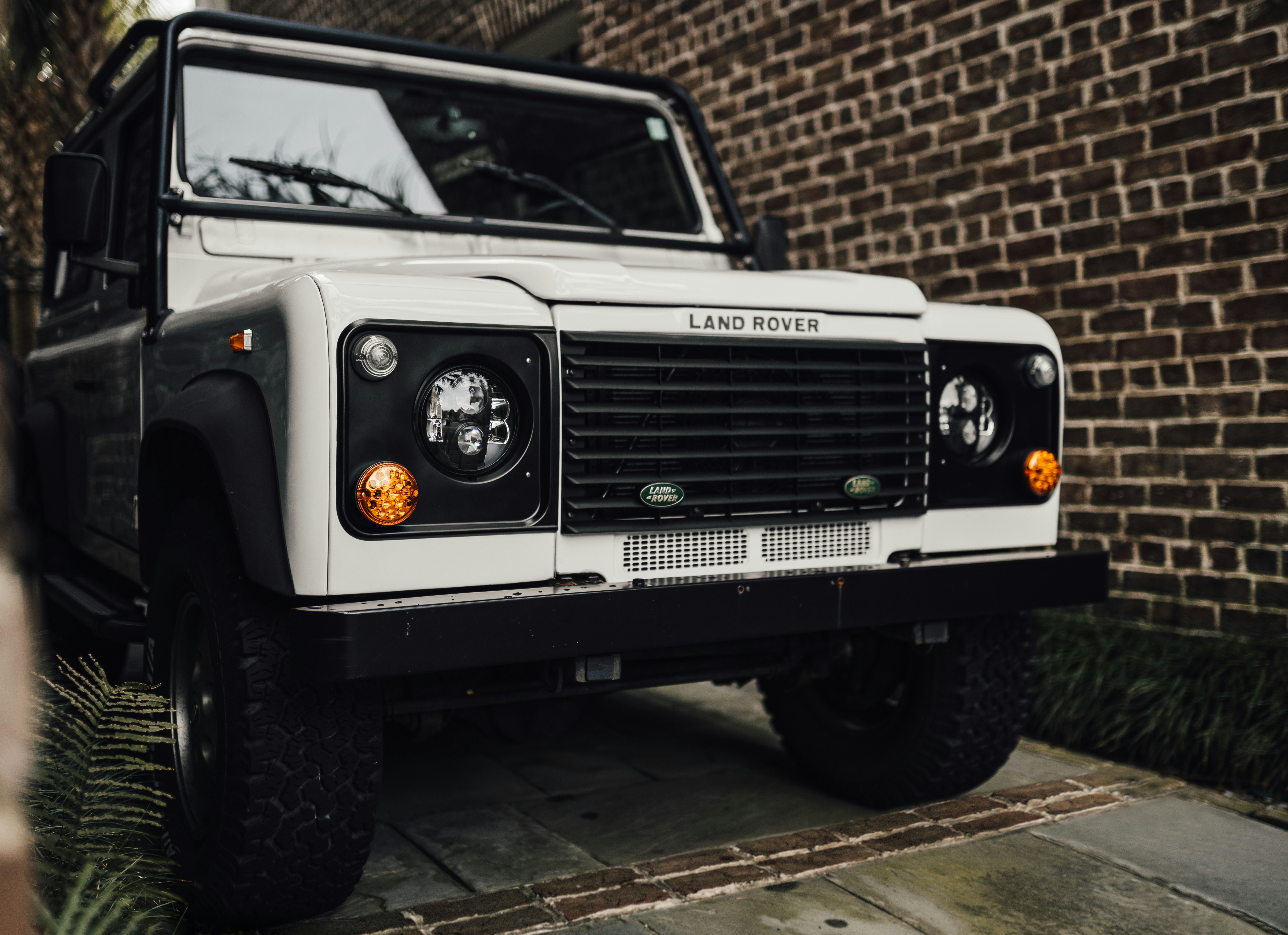 Front-Frame Defender: White Land Rover Braces a Brick-Walled Driveway