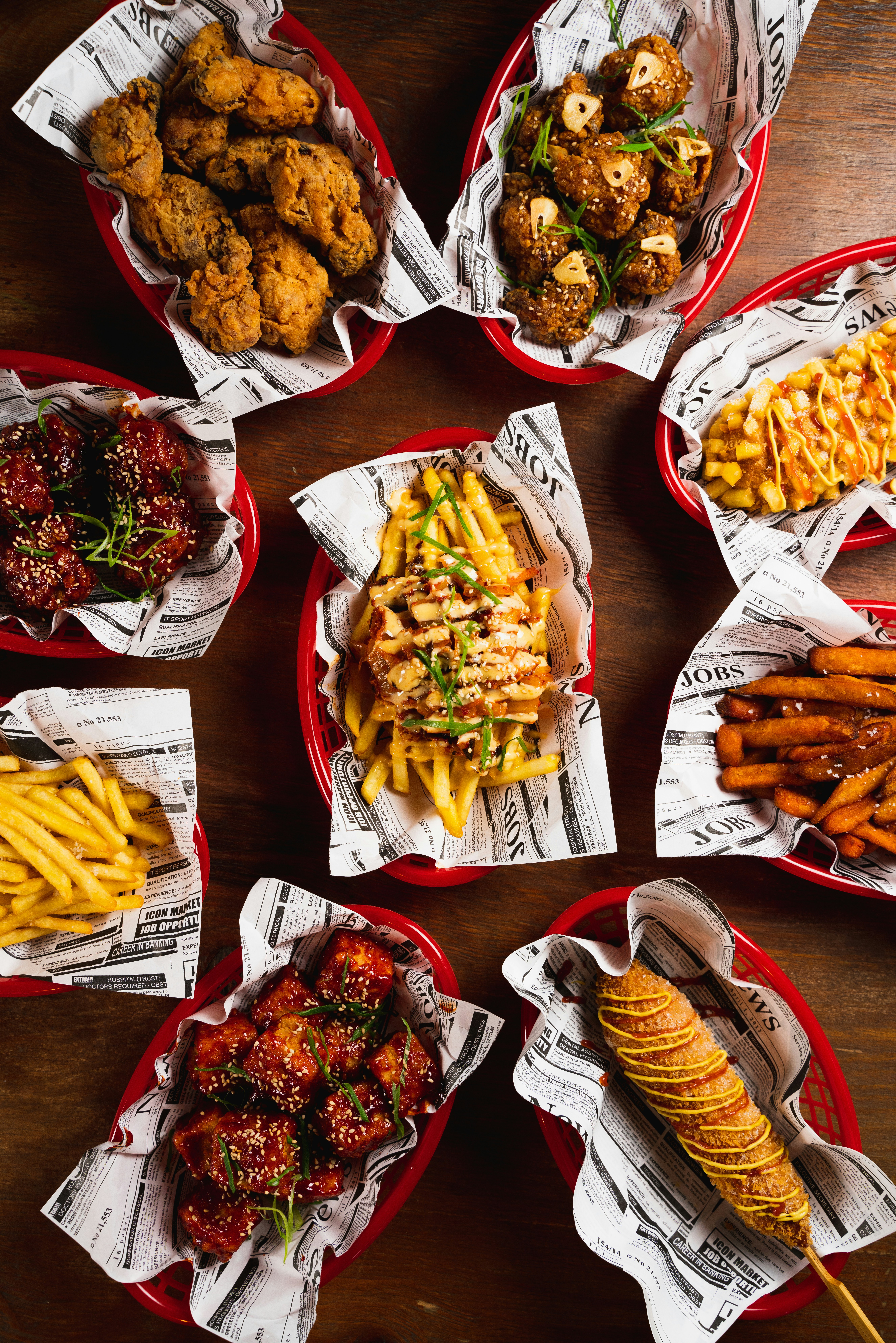 A vibrant spread of comfort foods featuring crispy fried chicken, savory meatballs, loaded fries, and more, all presented in red baskets lined with newspaper print.