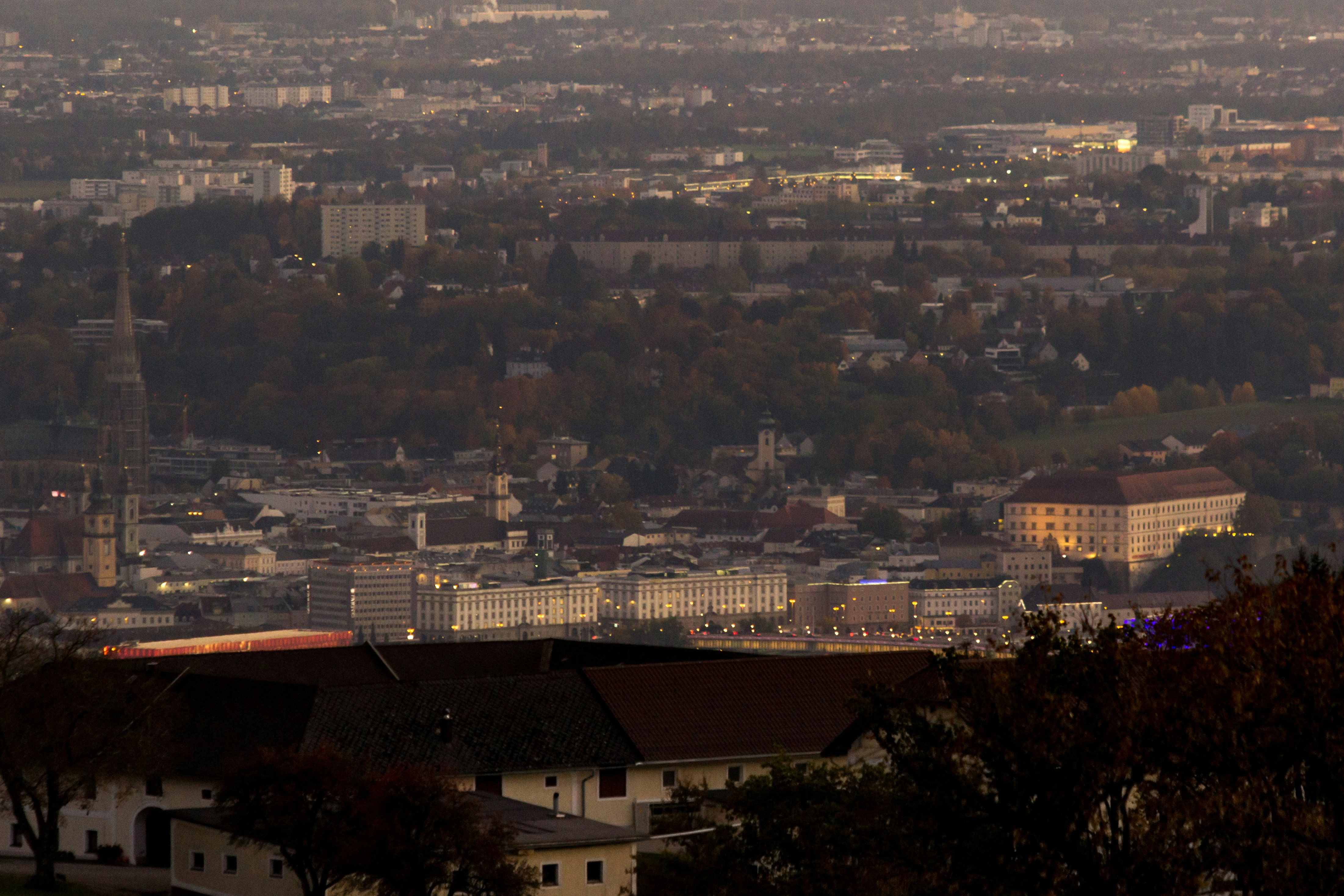 Expansive cityscape at dusk with buildings and distant hills under a hazy sky.