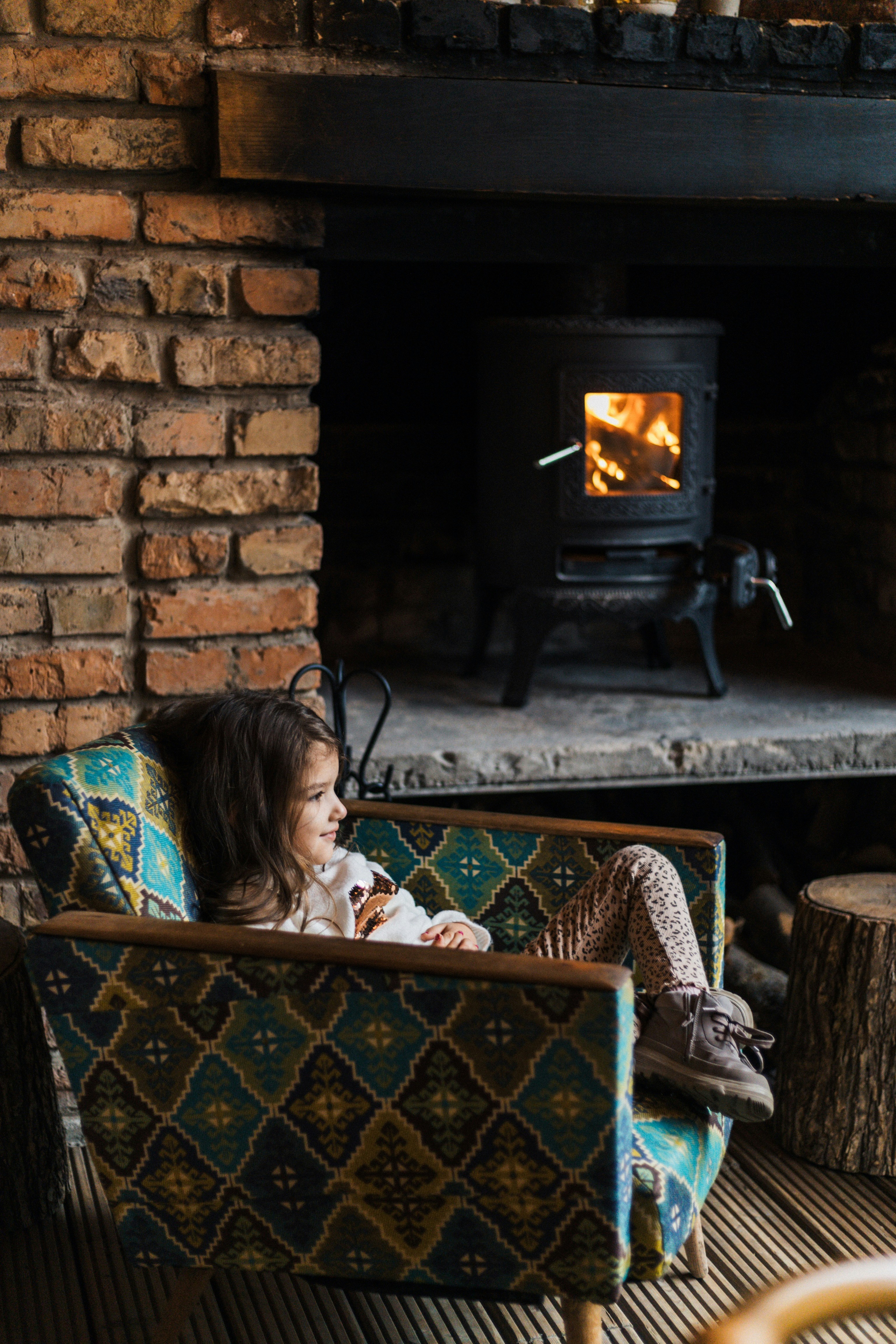 a little girl sitting in a chair in front of a fire place